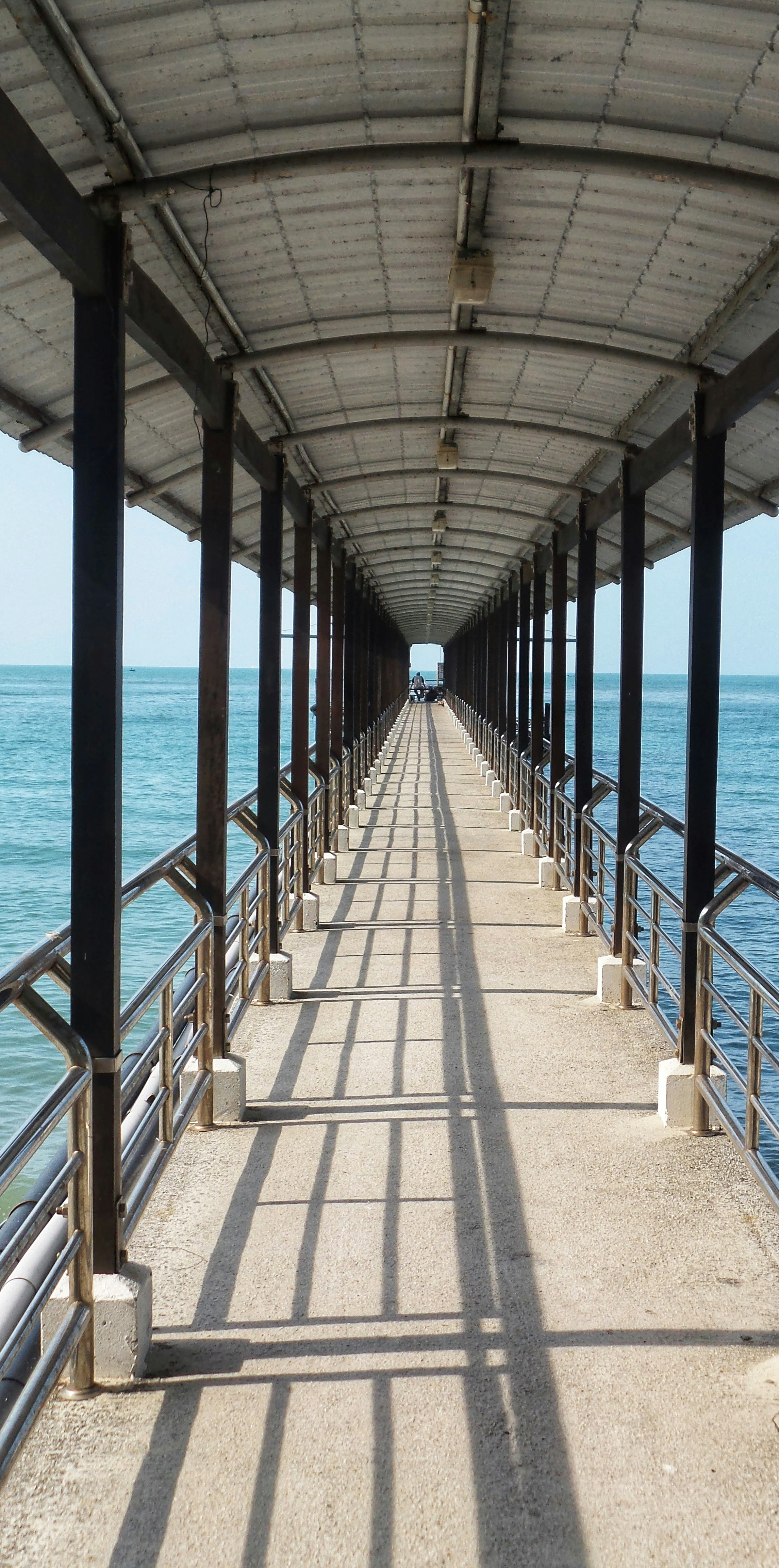 Long pier extending over turquoise waters, framed by supportive beams and shadows, inviting exploration.