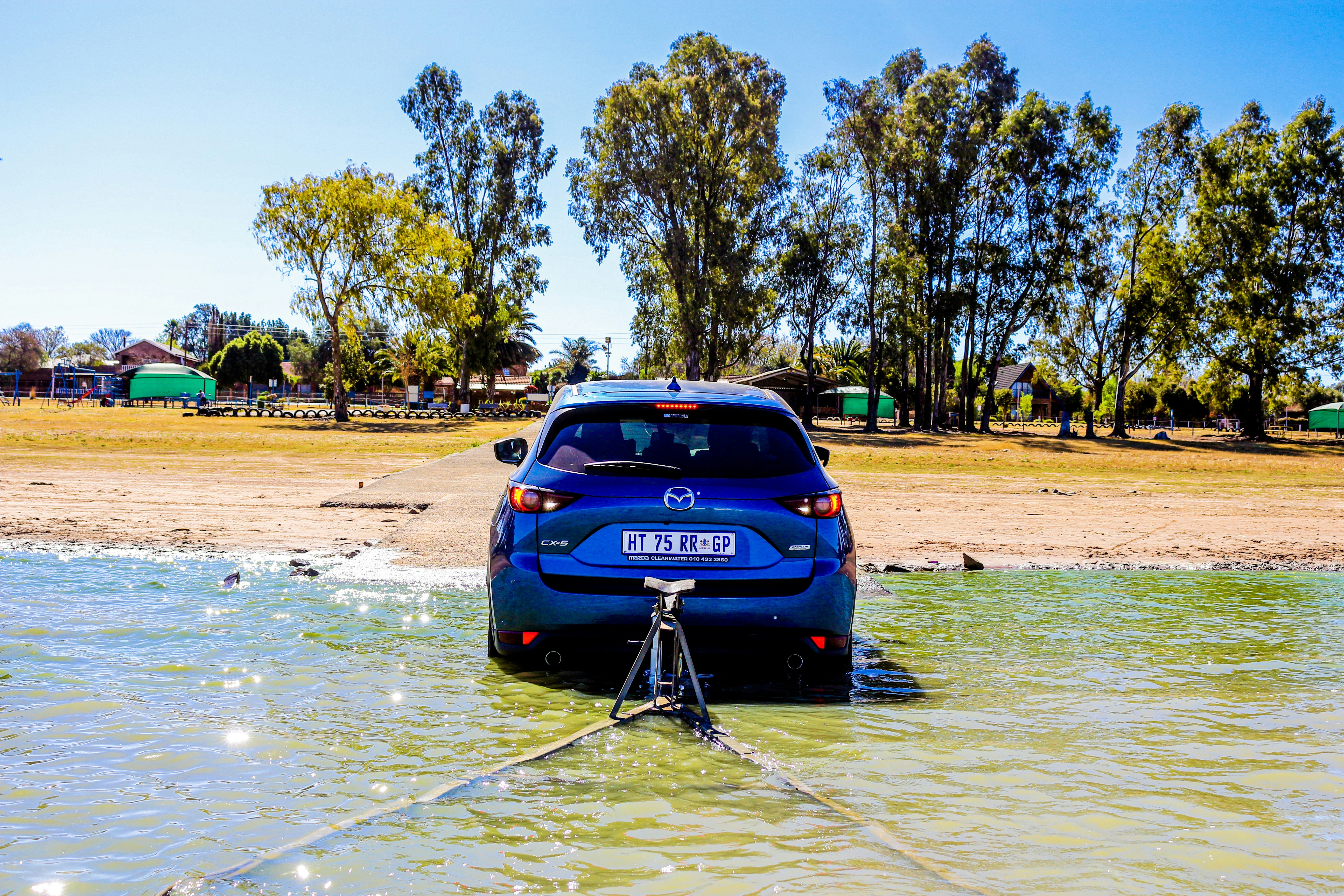 blue Mazda vehicle with rope on it's back on body of water near trees during day