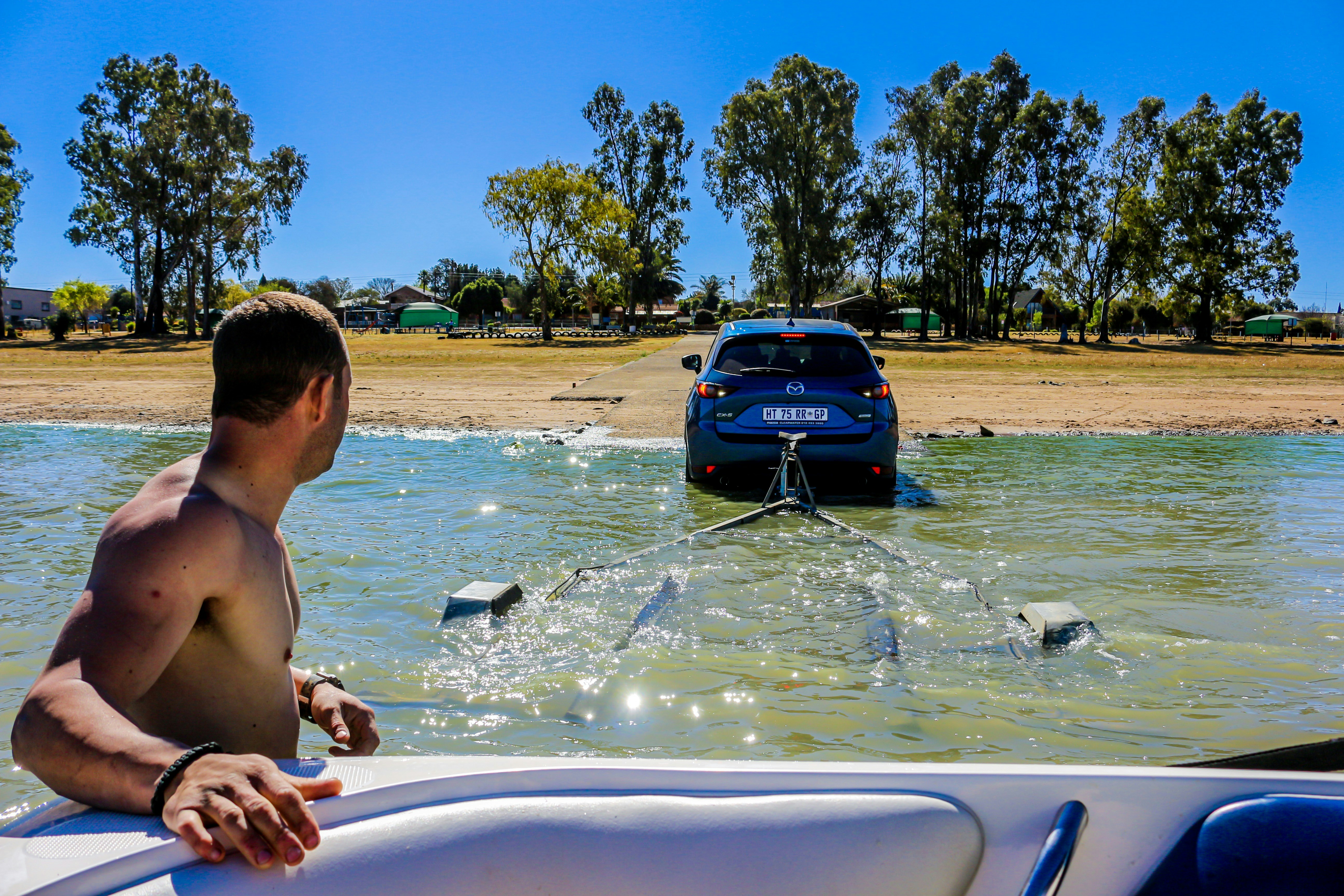 Blue SUV Anchored in a Shallow Lake, Framed by a Foreground Boatman