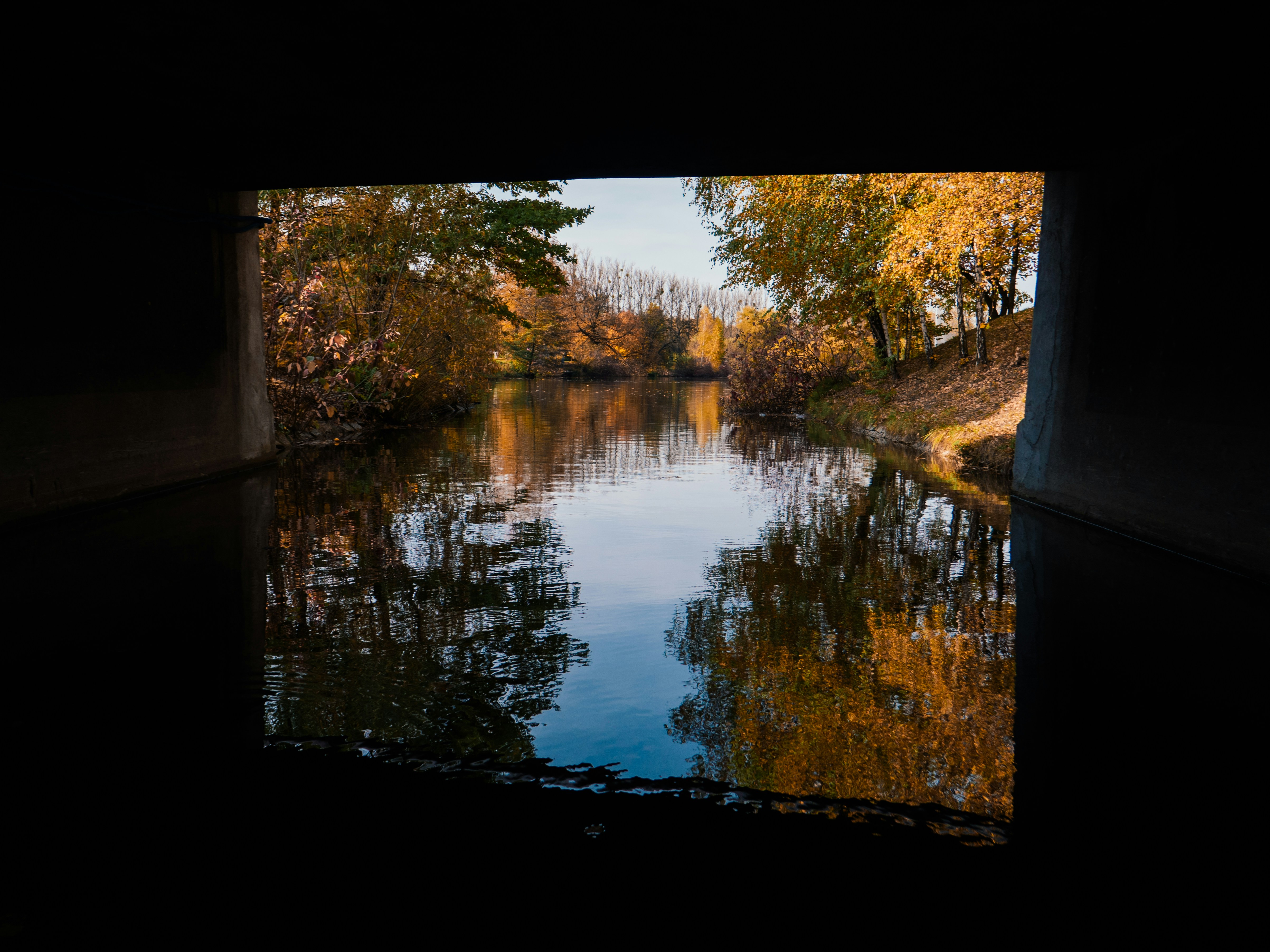 Exit Through Autumn: River Reflections Framed by a Dim Arch