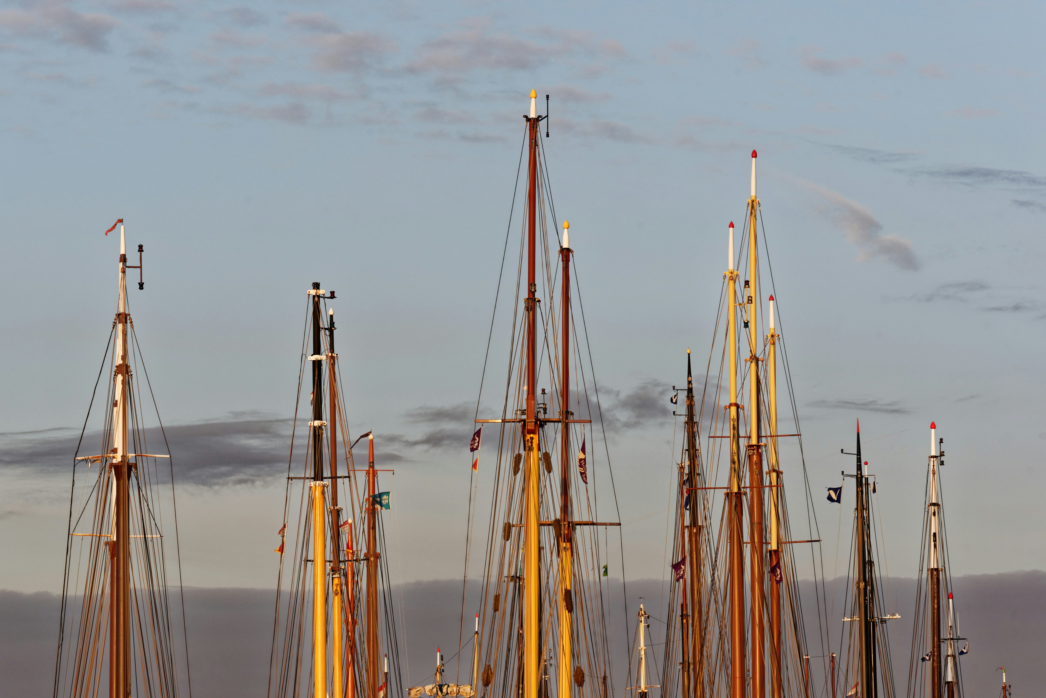 Tall ship masts silhouetted against a softly lit sky with scattered clouds.