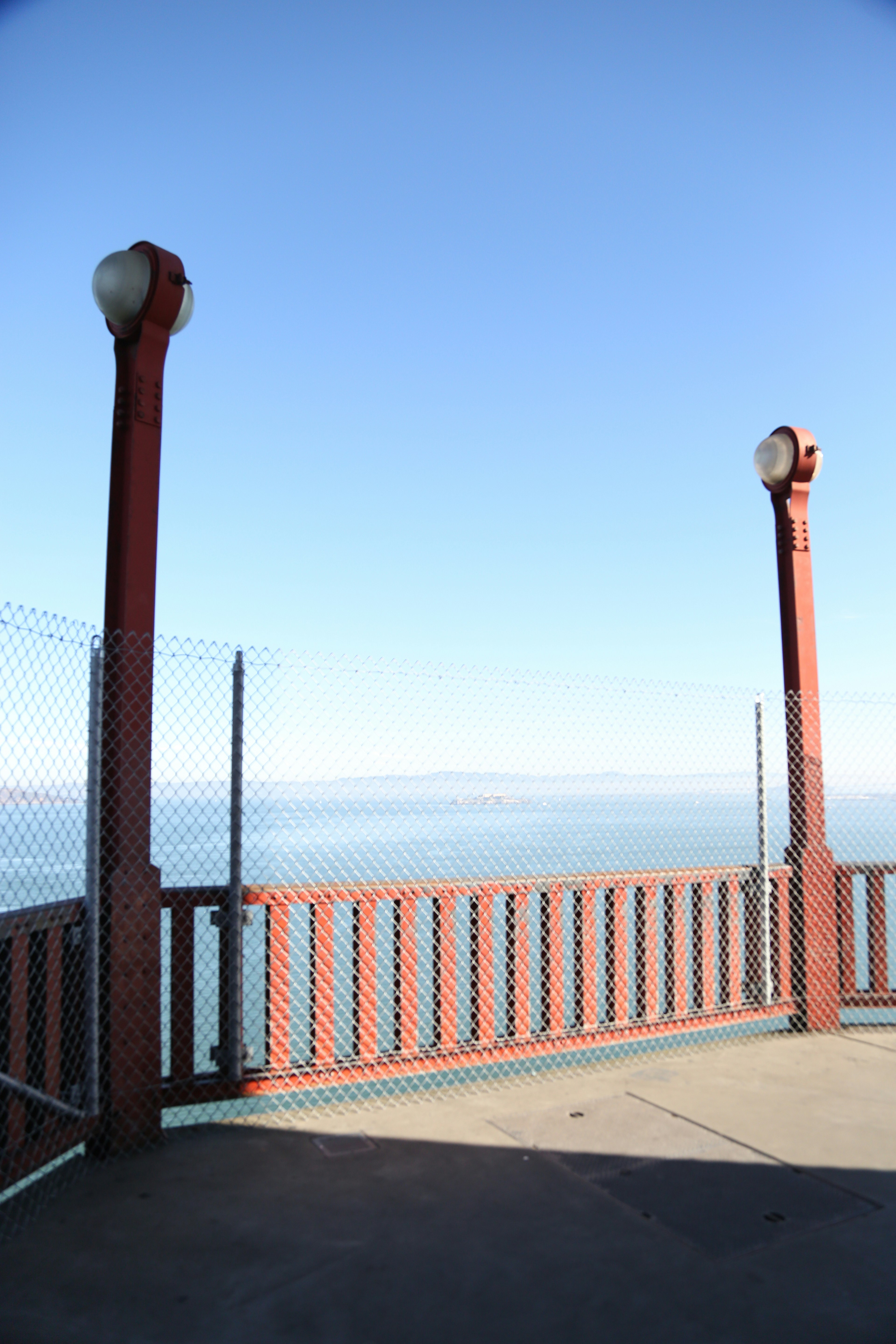 Vantage point overlooking the bay from a bridge, framed by red railings and light fixtures. The serene waters stretch toward distant hills.