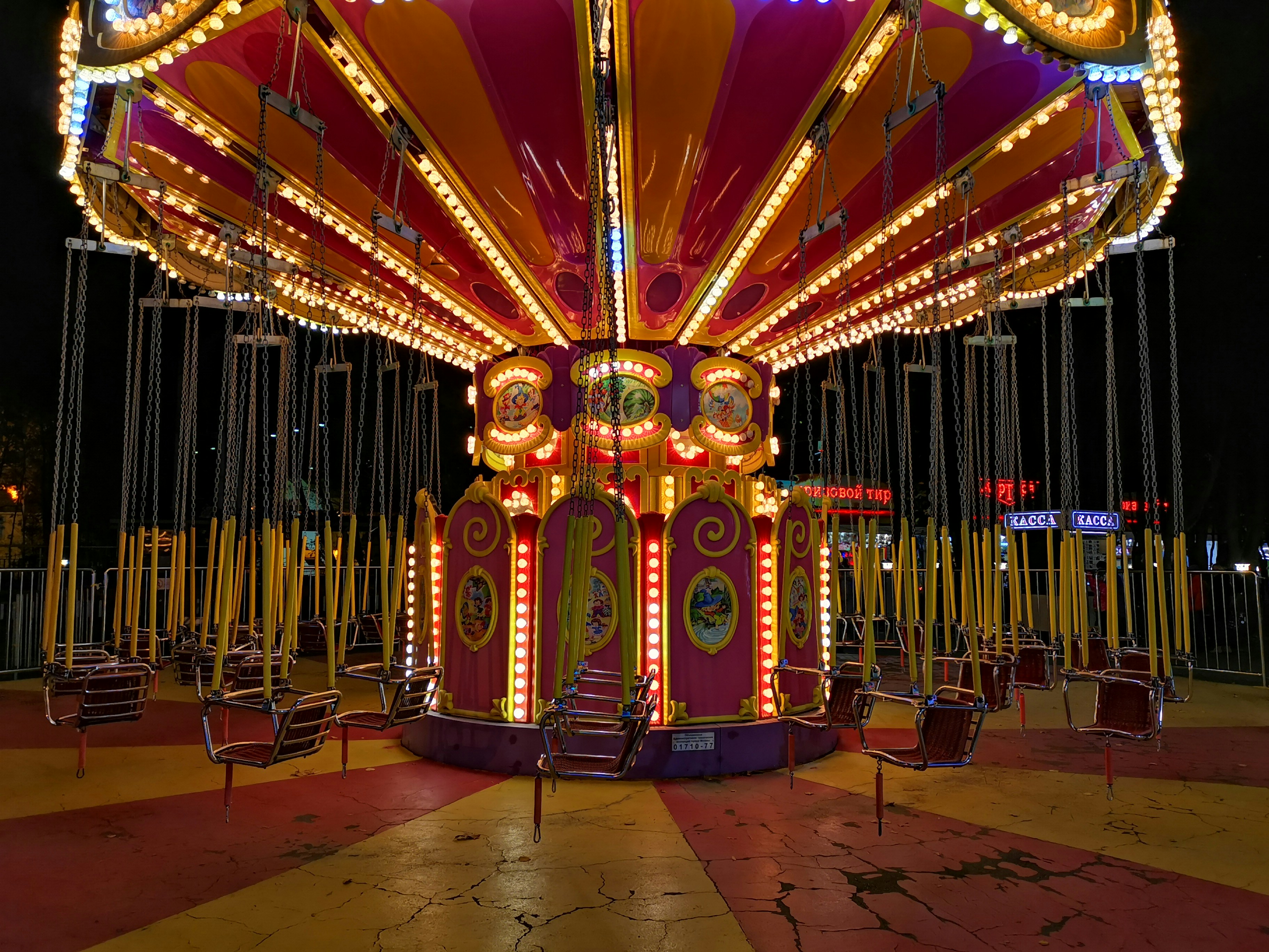Colorful swing ride illuminated by vibrant lights at night, showcasing an empty seating arrangement. The playful atmosphere evokes nostalgia for carnival fun.