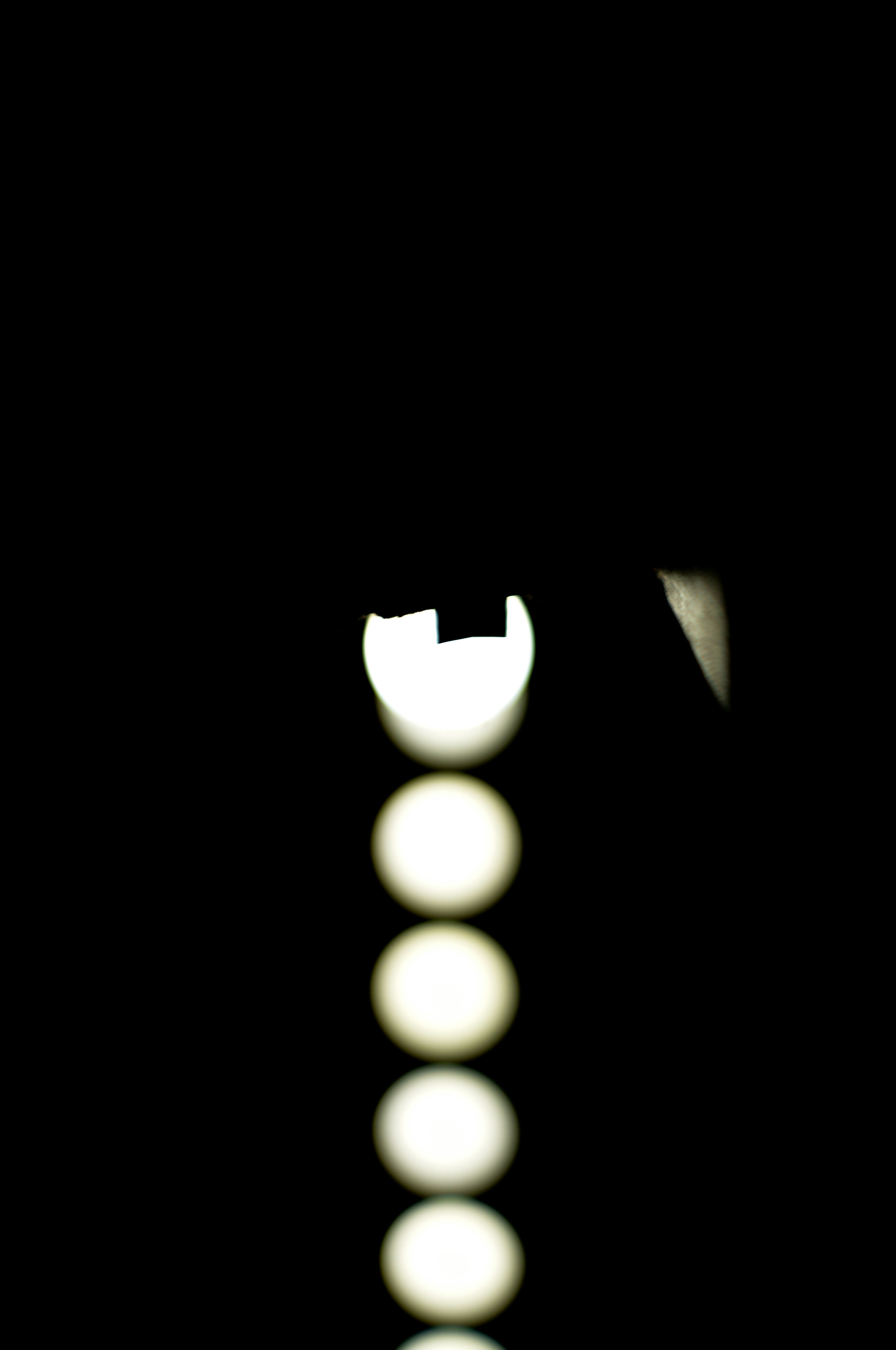 Abstract representation of light cascading through a narrow opening, creating a series of glowing orbs against a dark backdrop.