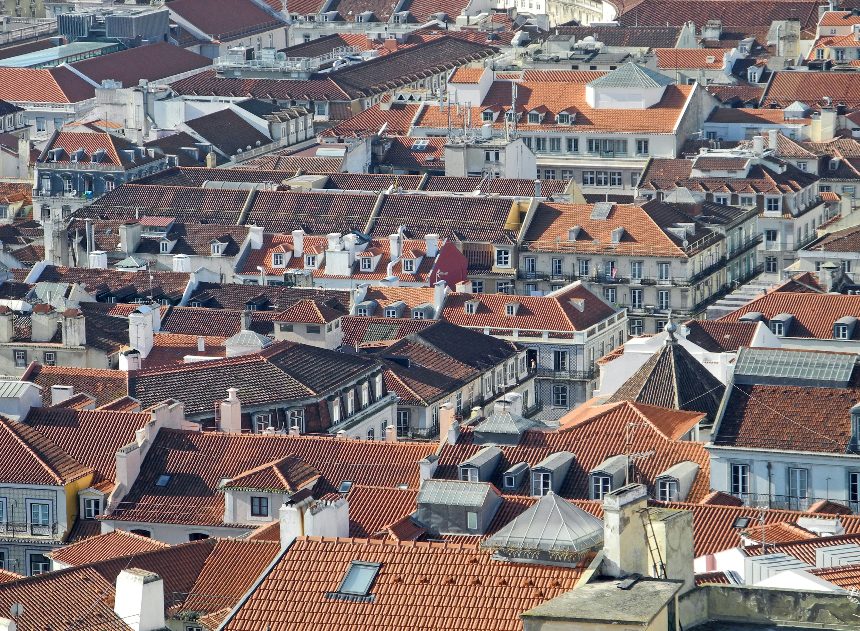 Aerial view of Lisbon's rooftops showcasing a vibrant collection of terracotta tiles and varied architectural styles. The intricate patterns create a harmonious urban landscape.