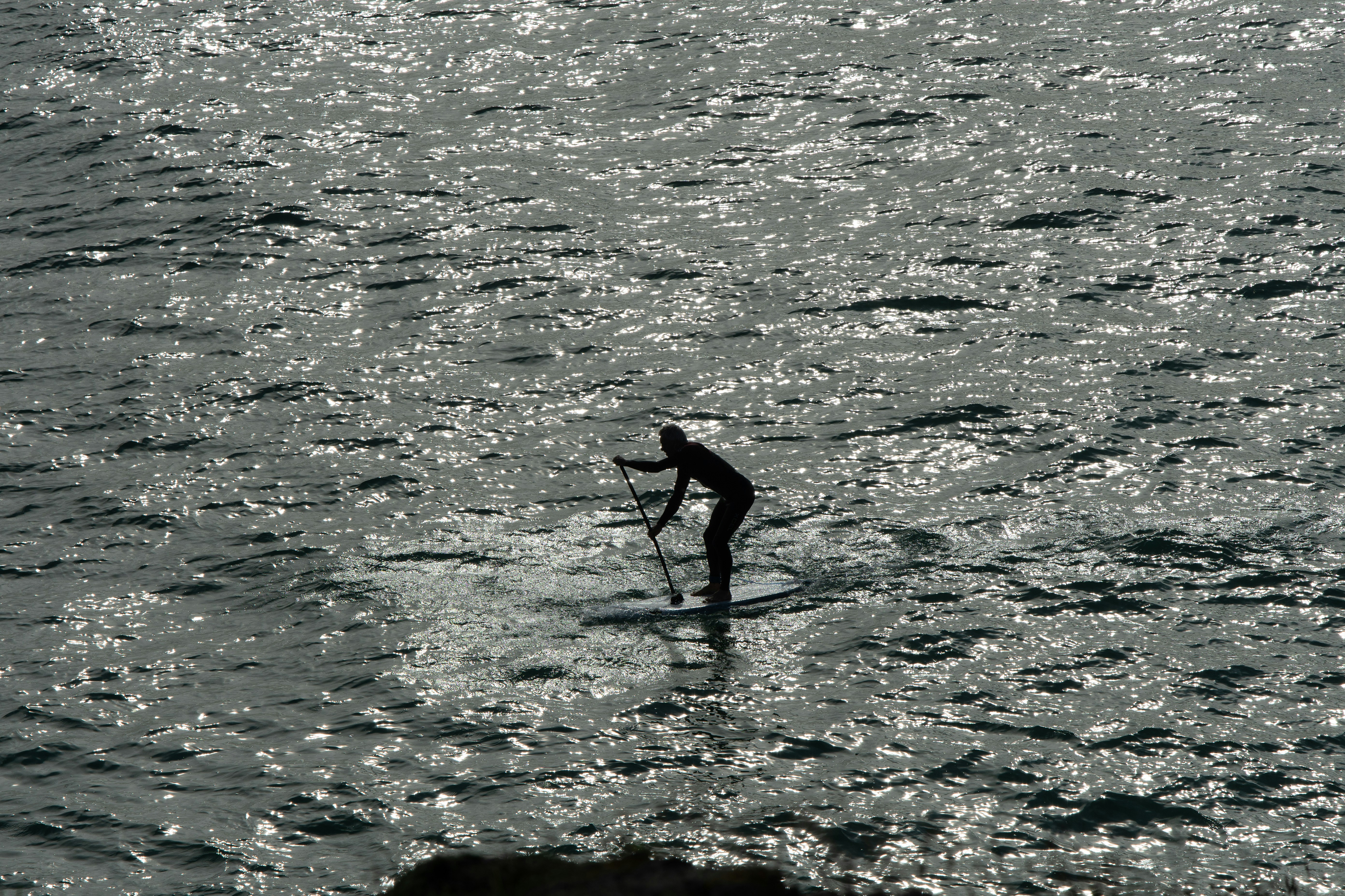 A paddle boarder in Cornwall, UK. | man riding white sailboat on middle ocean