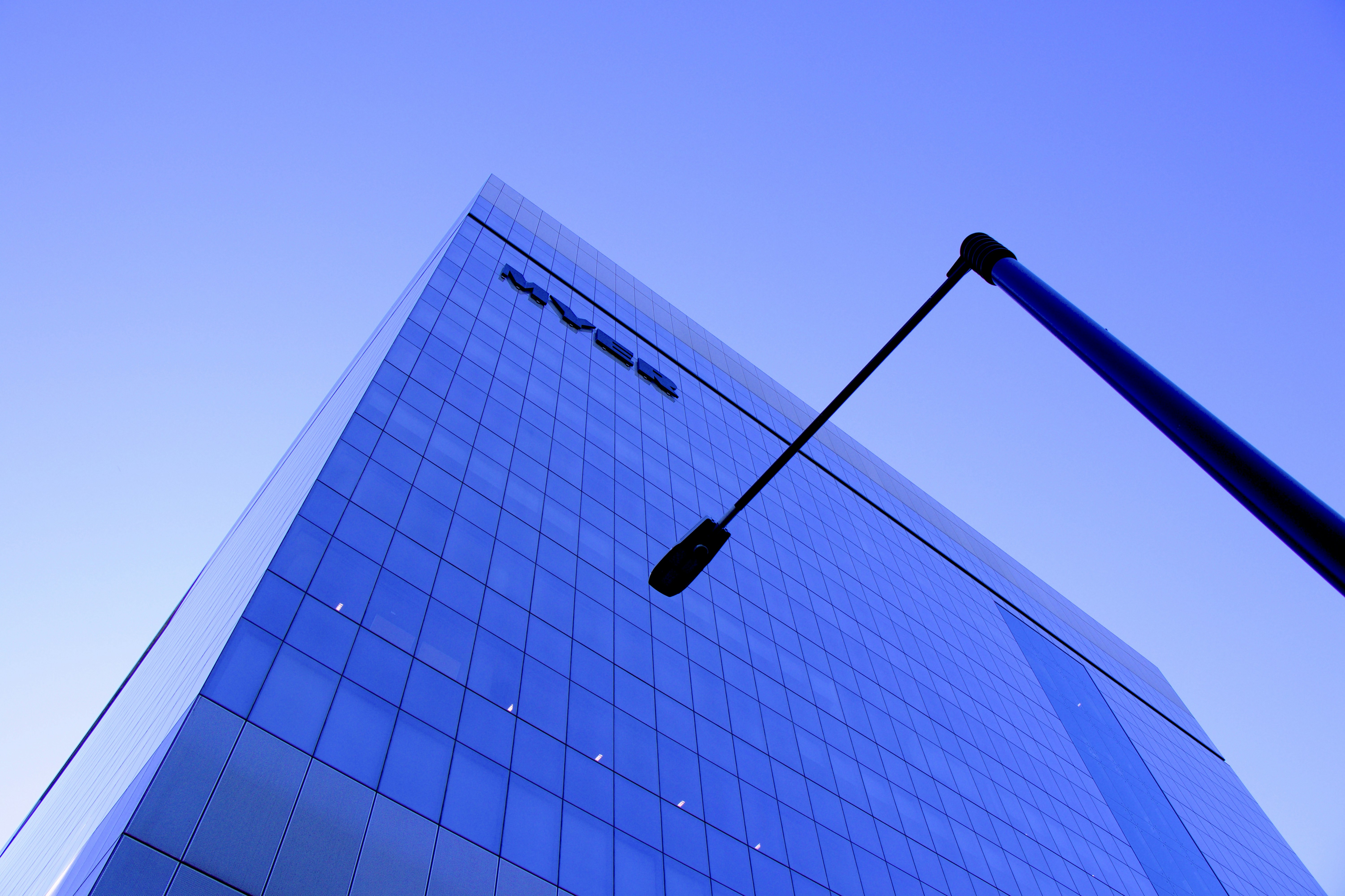 A modern glass skyscraper reflects the evening sky, framed by a streetlight in the foreground.