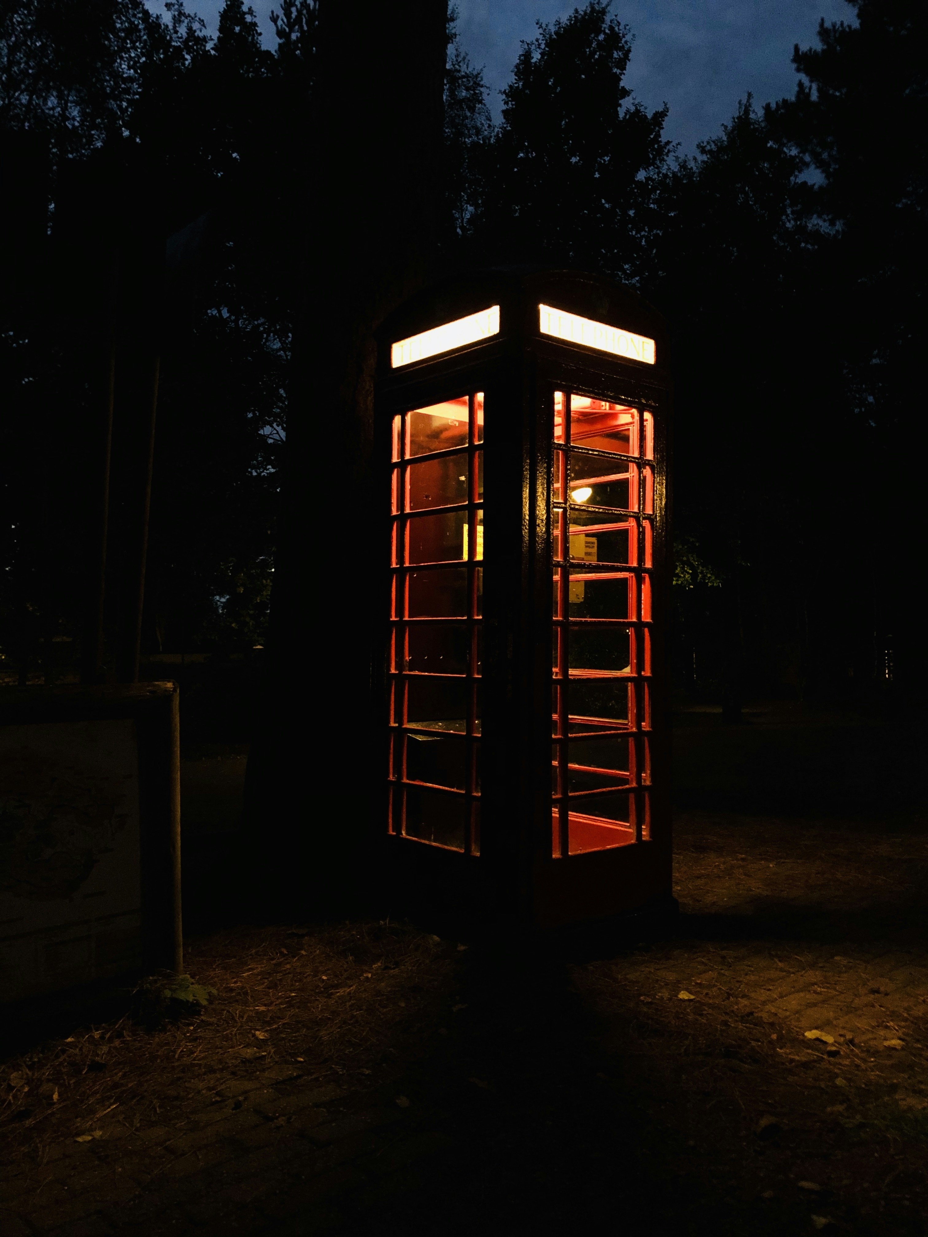 Crimson Phone Booth in the Night: A Park Beacon of Warm Light