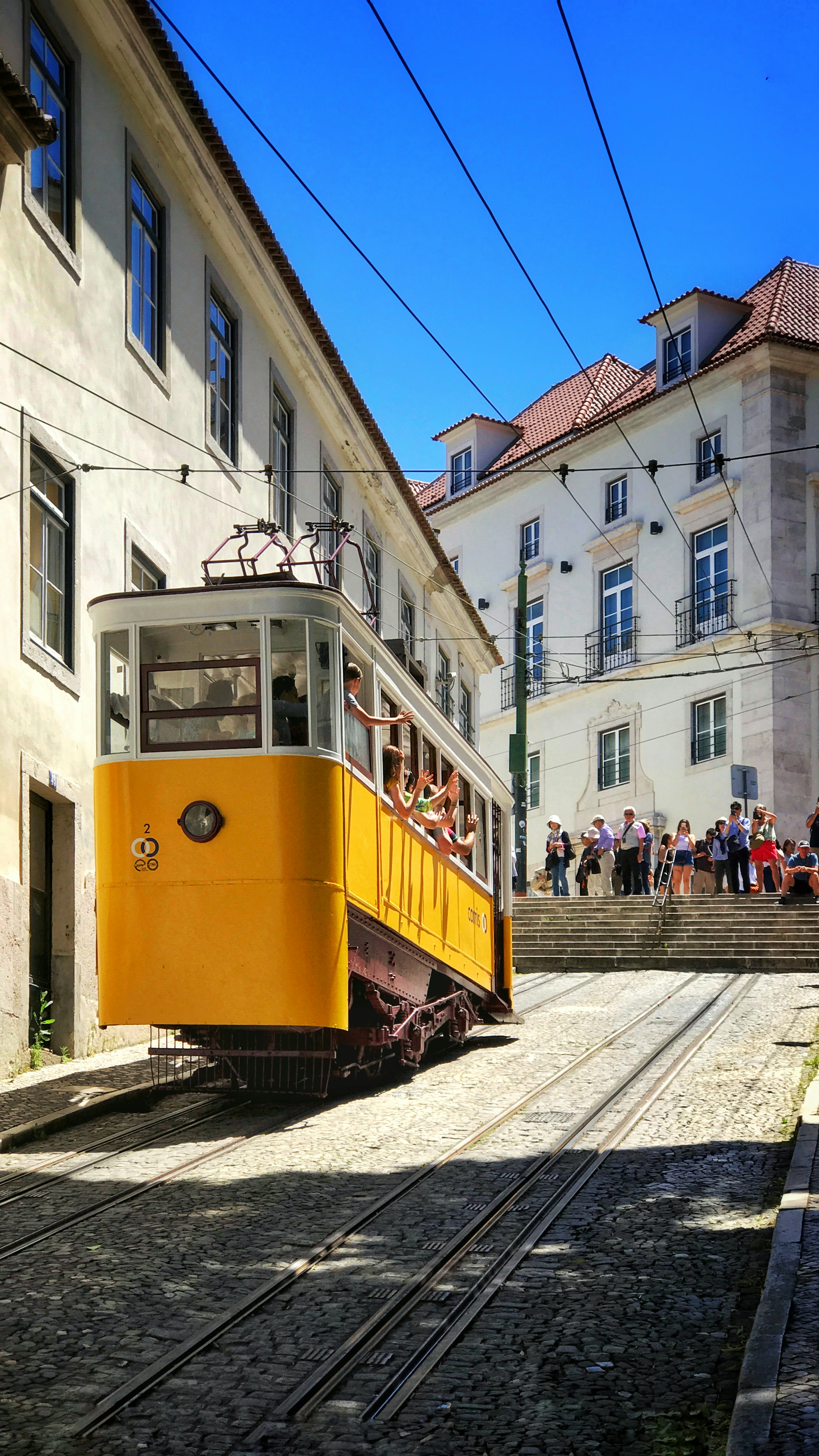 Sunlit Yellow Tram Climbing a Cobblestone Hill Among White Historic Facades