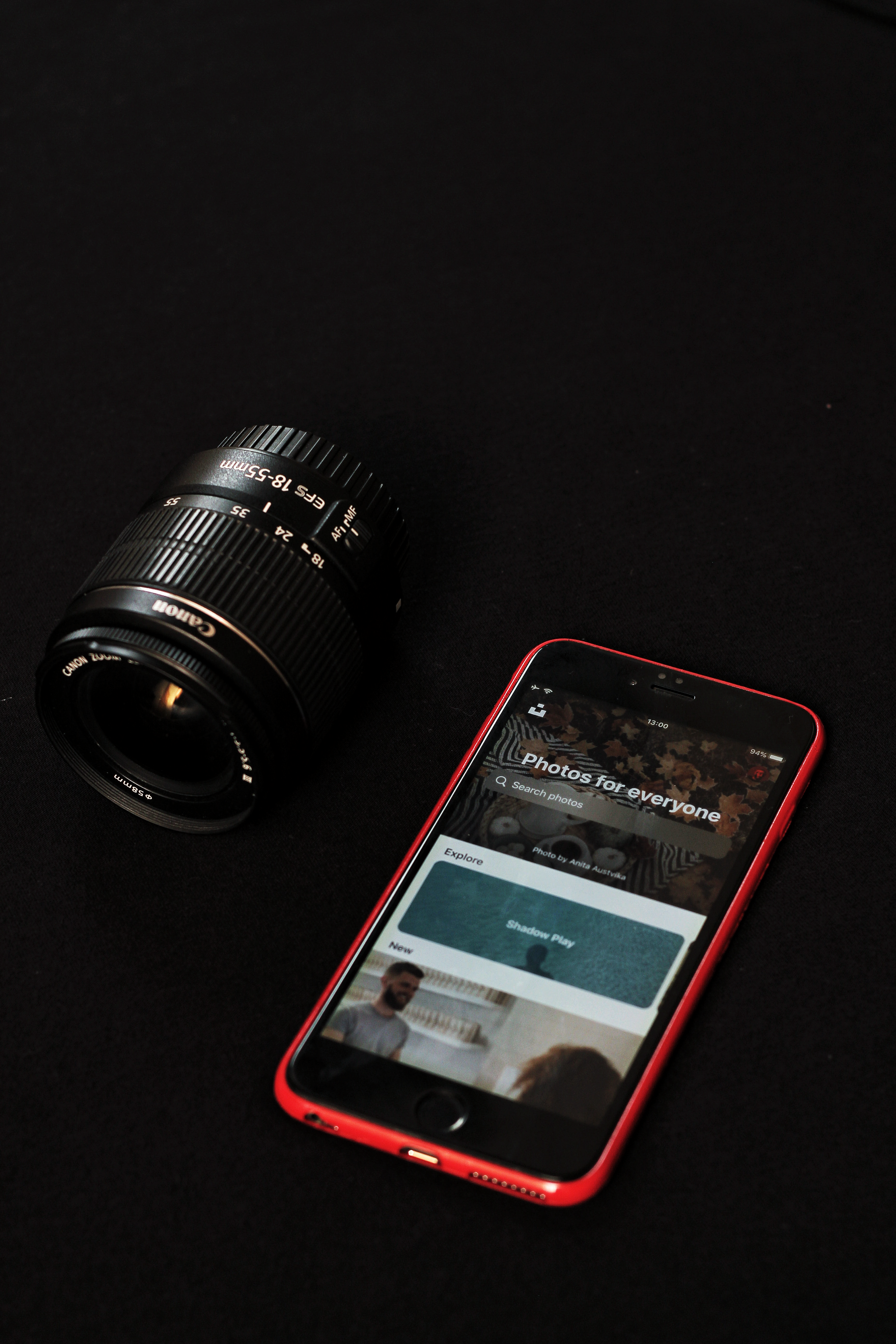 A Canon lens and a smartphone displaying a photography app, showcasing tools for capturing moments. The setup is placed on a dark surface.