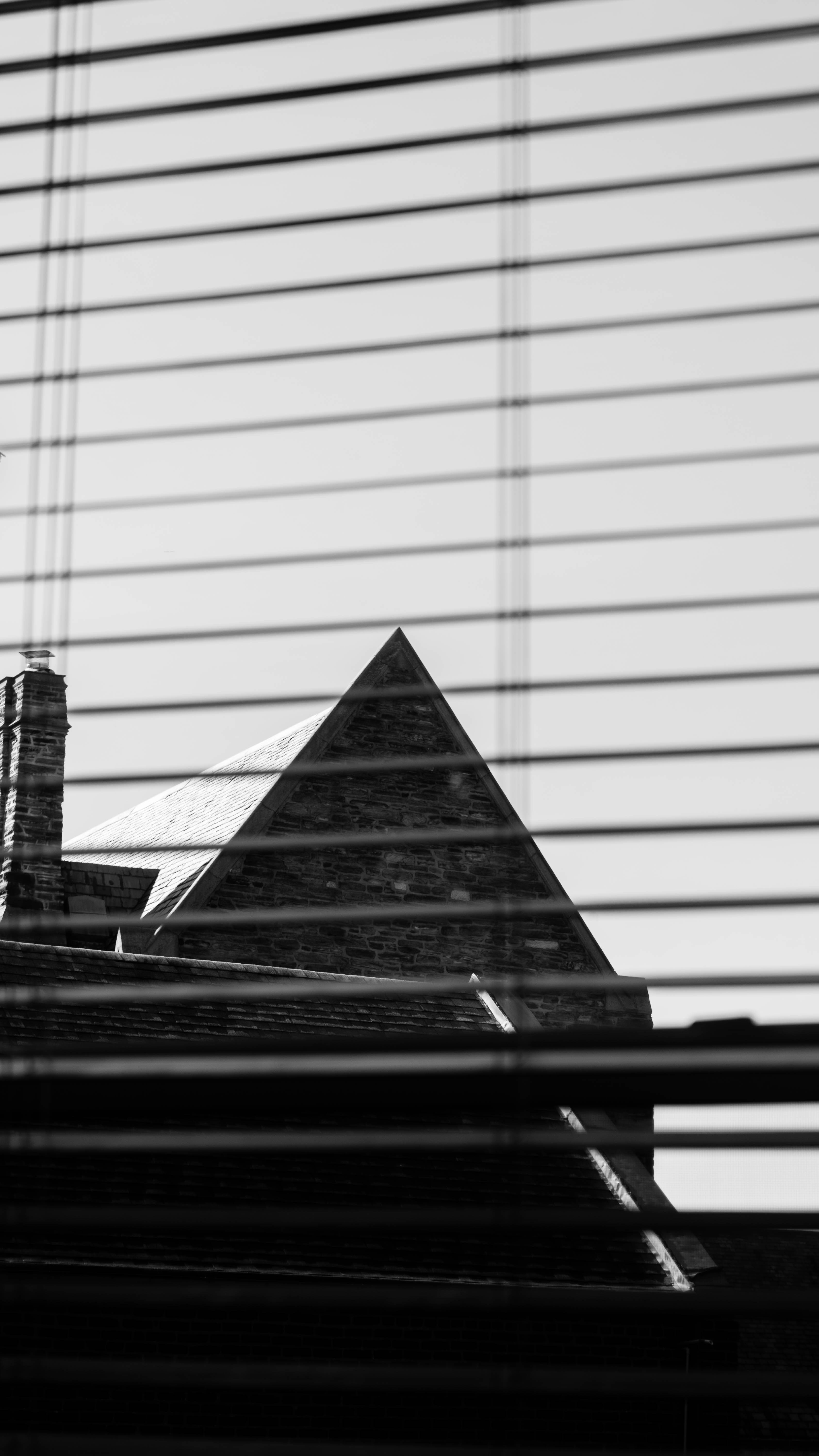 A triangular roof silhouette partially obscured by horizontal blinds, creating a striking contrast of light and shadow.
