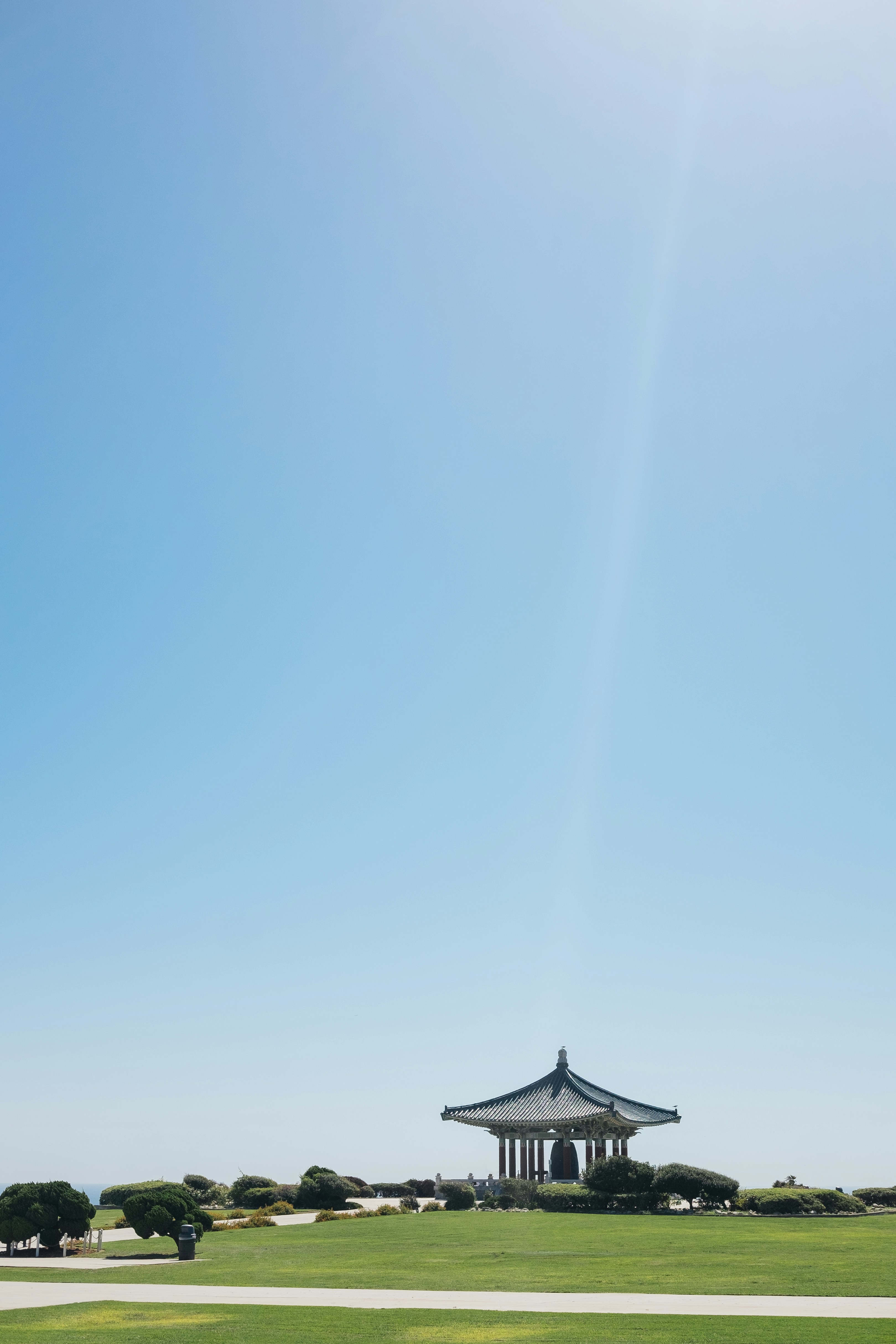 Korean Friendship Bell pavilion surrounded by lush greenery under a clear blue sky.