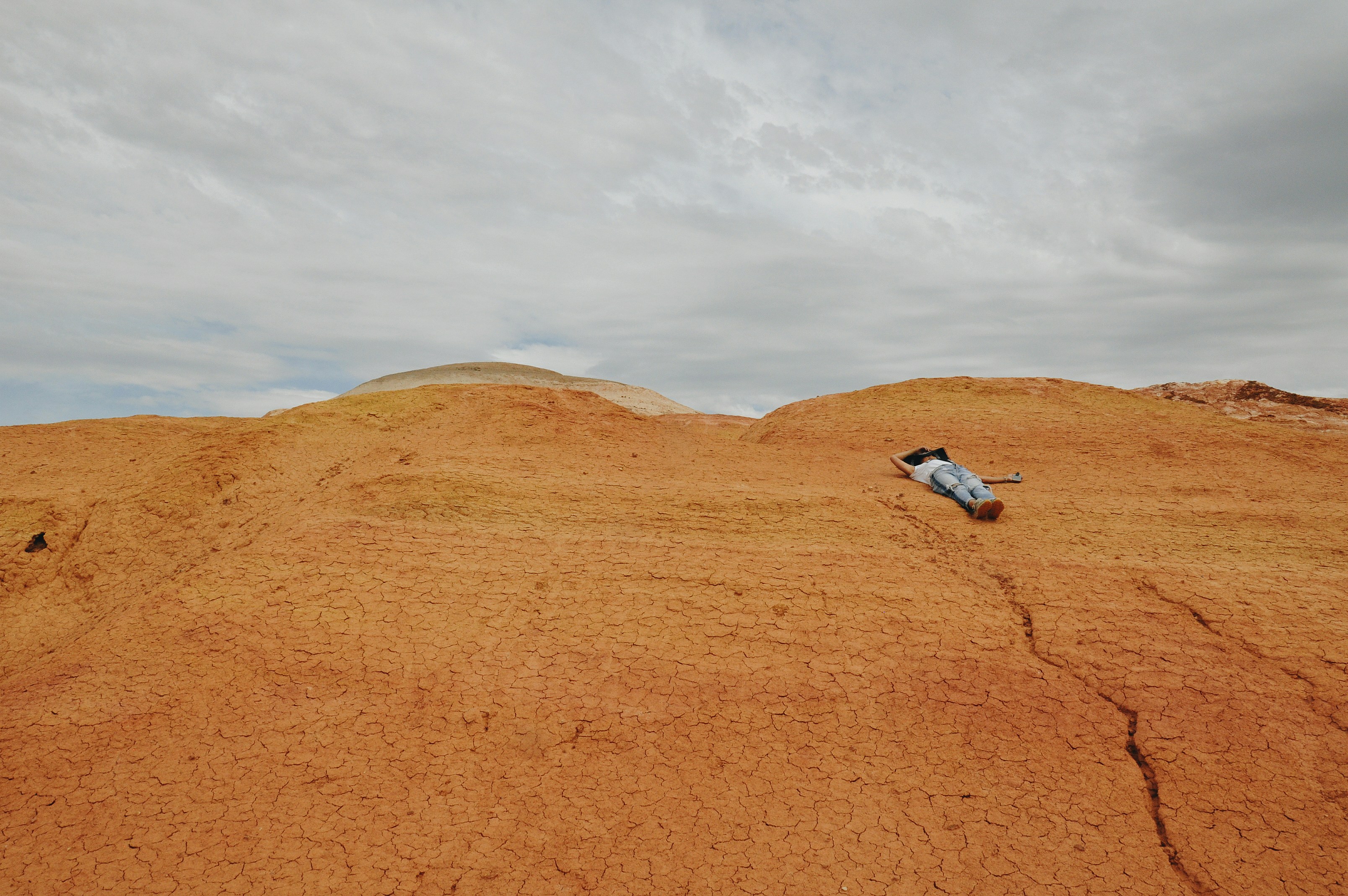 person wearing white shirt and blue denim jeans lying on rock formation