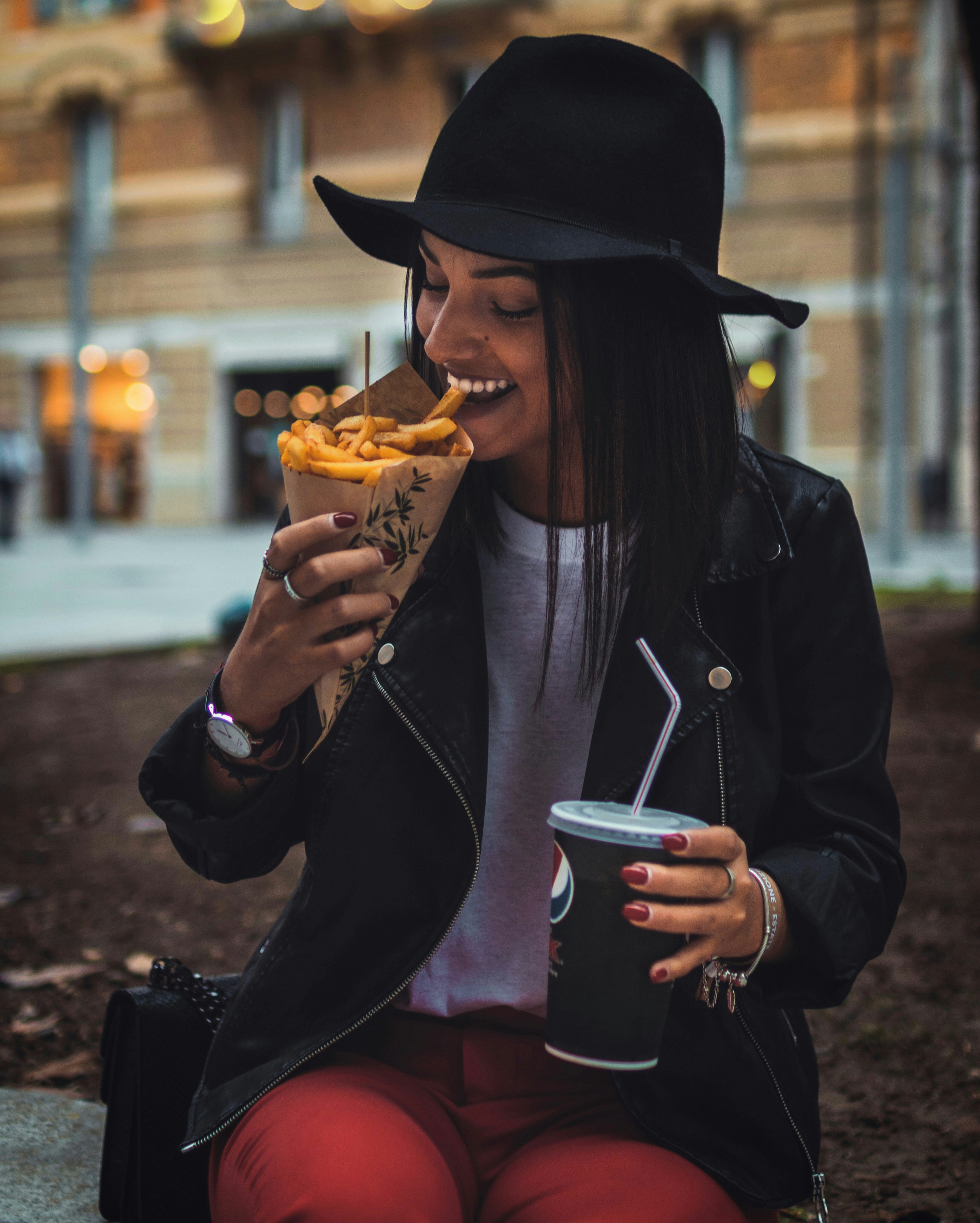 A woman sitting on a bench eating a sandwich and fries photo – Free ...