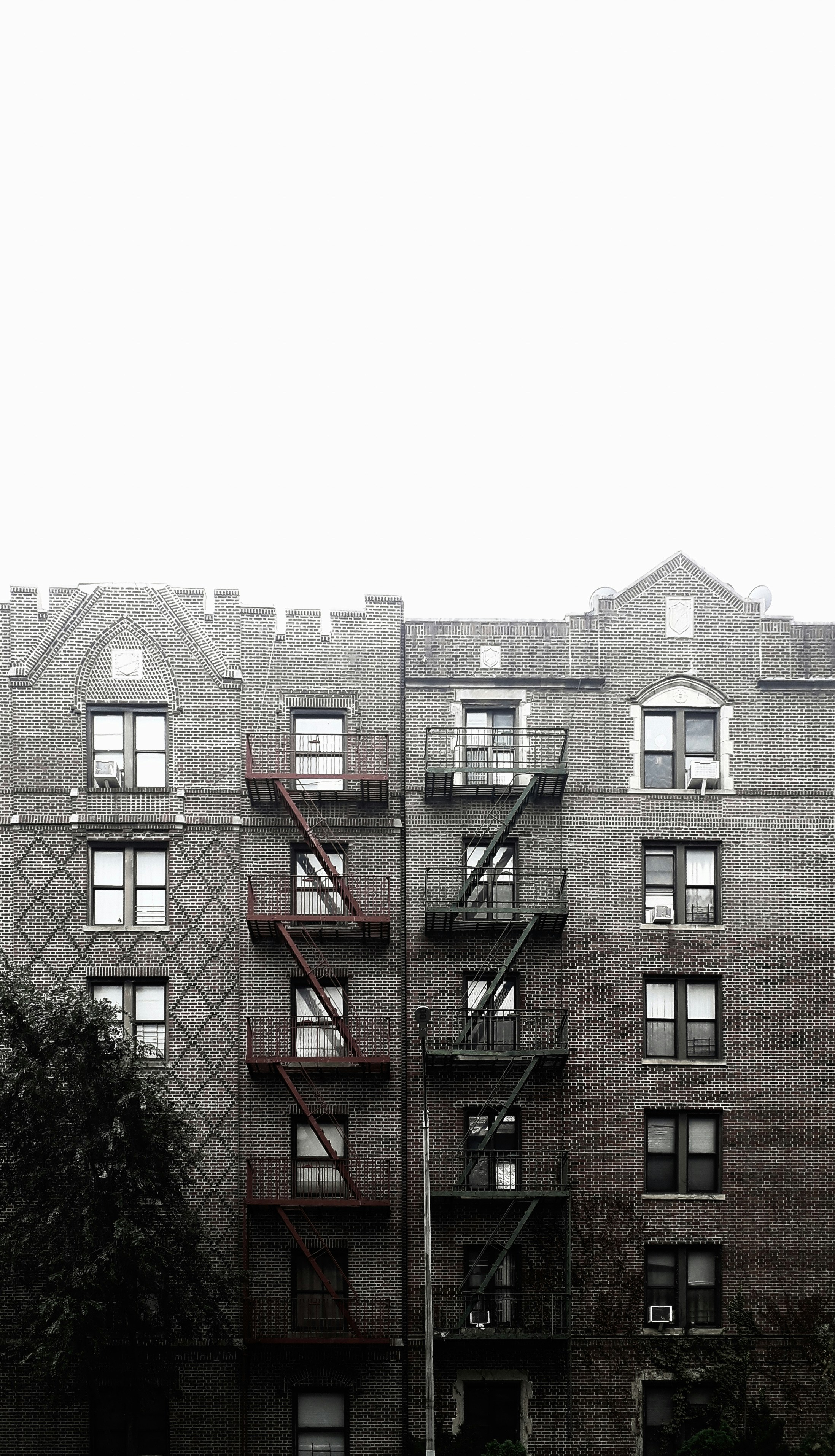 A brick apartment building featuring fire escapes and distinct architectural details, set against a stark white sky.