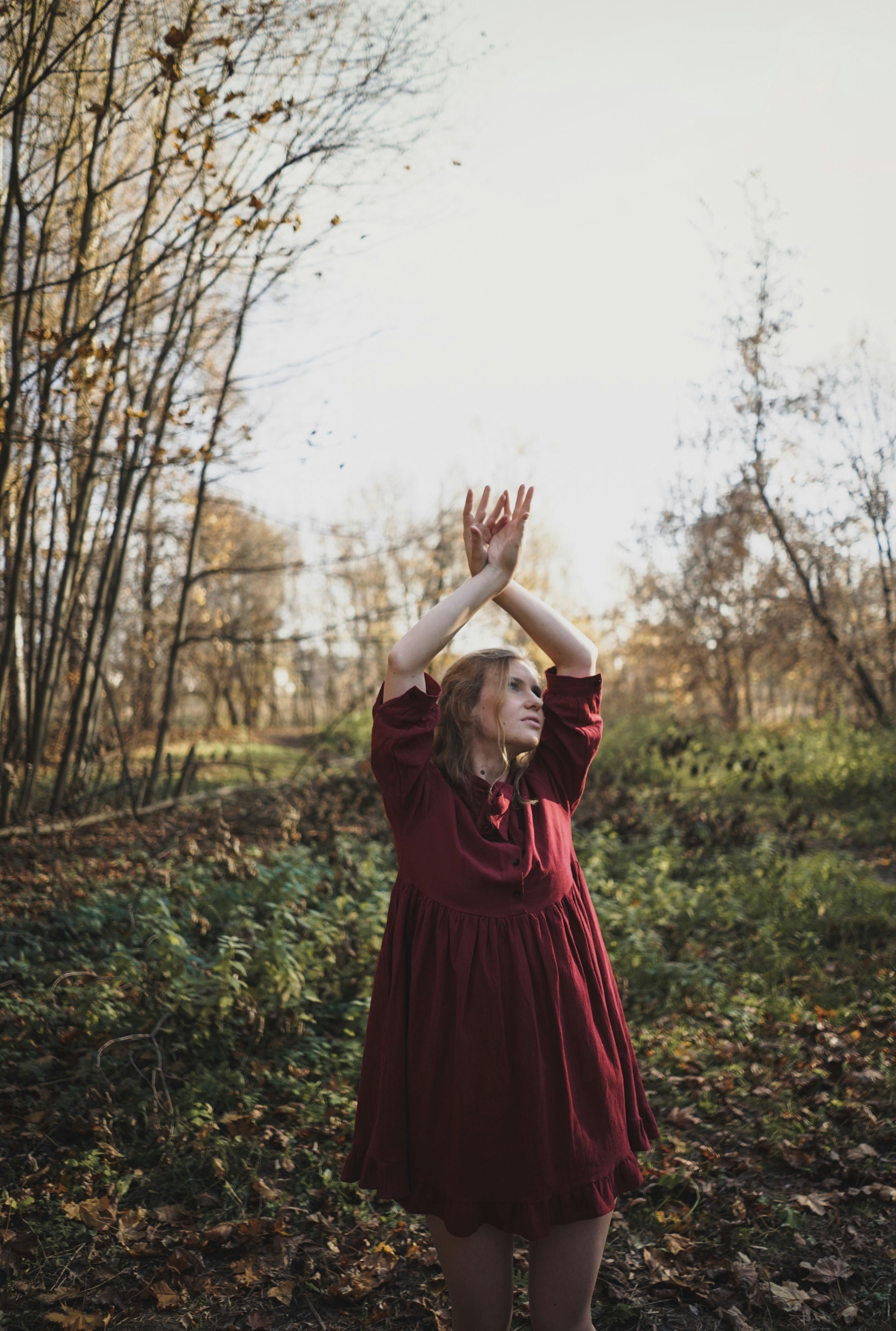 Woman in a flowing red dress poses gracefully amidst a sunlit forest, surrounded by autumn foliage.