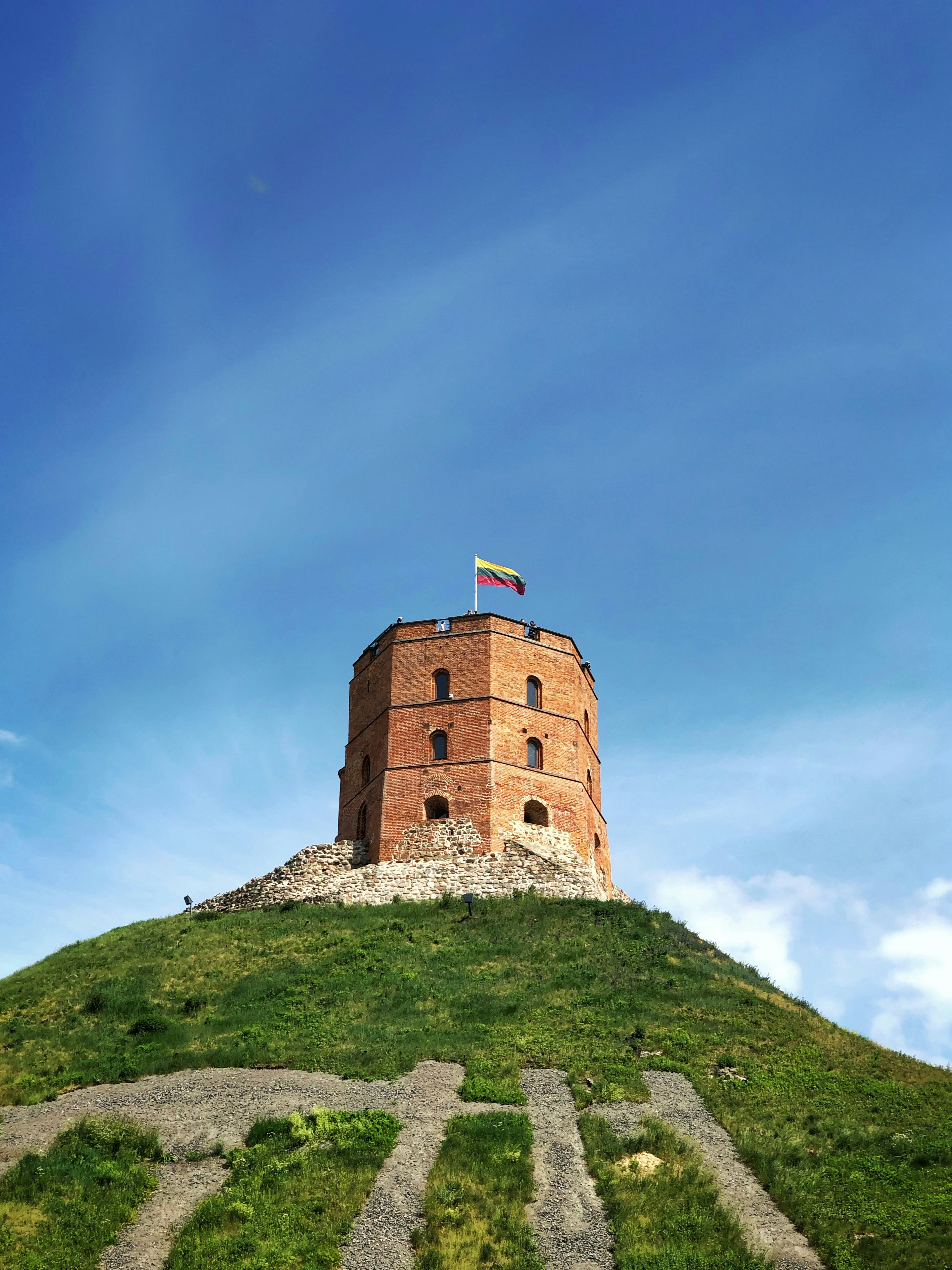 Historic tower perched atop a grassy hill, adorned with a waving flag against a clear blue sky.