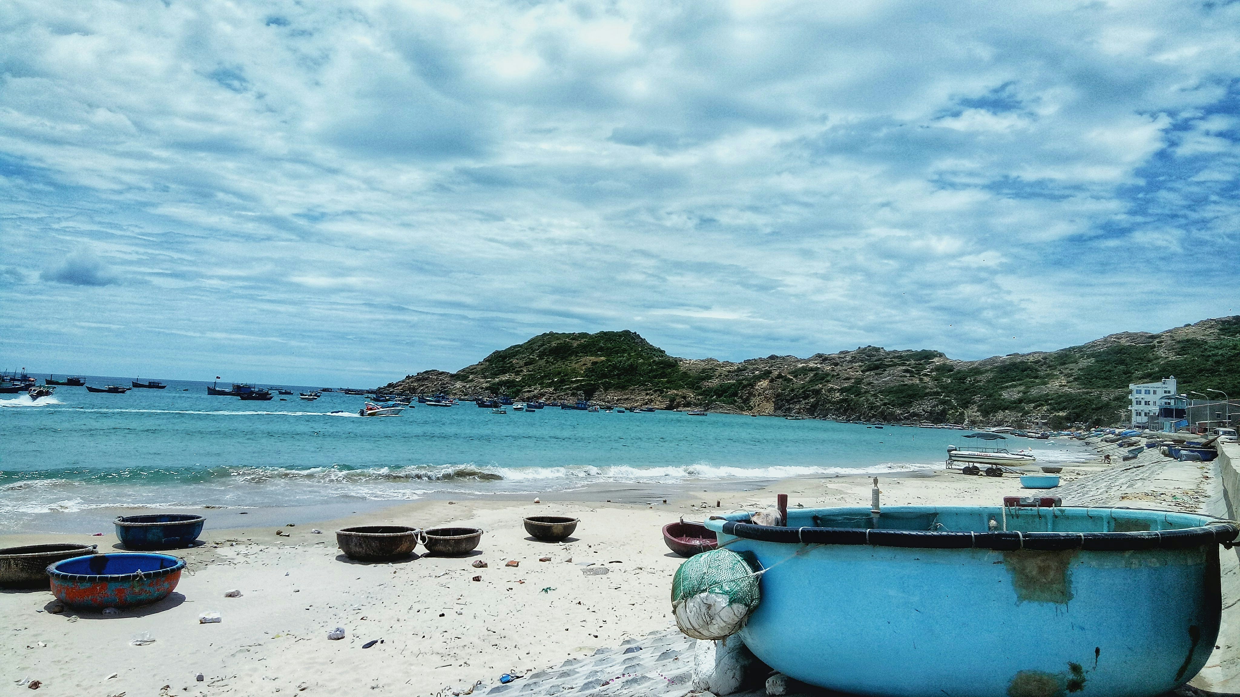 Circular boats resting on a sandy beach with turquoise waters and distant hills under a cloudy sky.