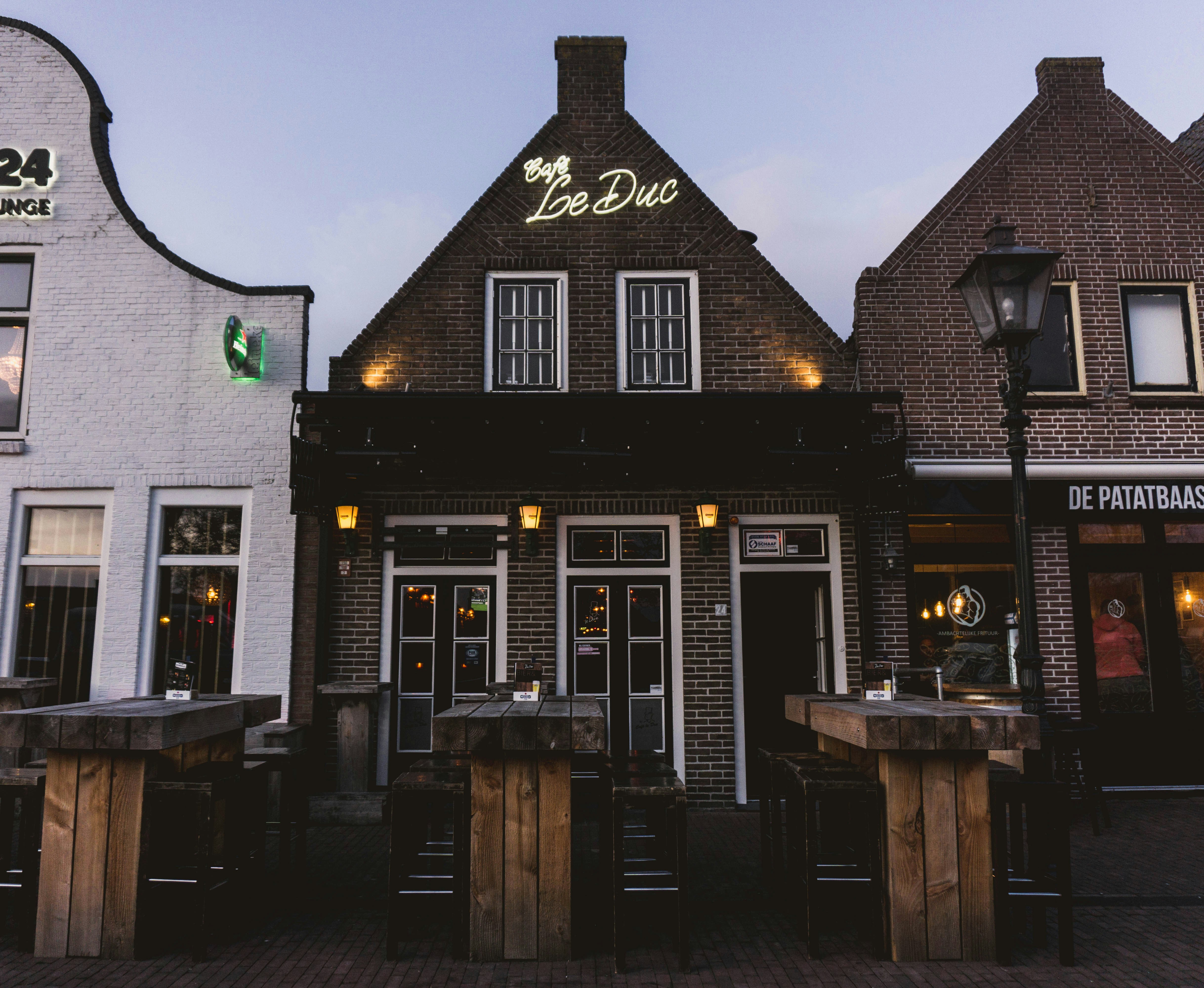 Charming tavern facade illuminated at dusk, showcasing a welcoming atmosphere with wooden tables outside.