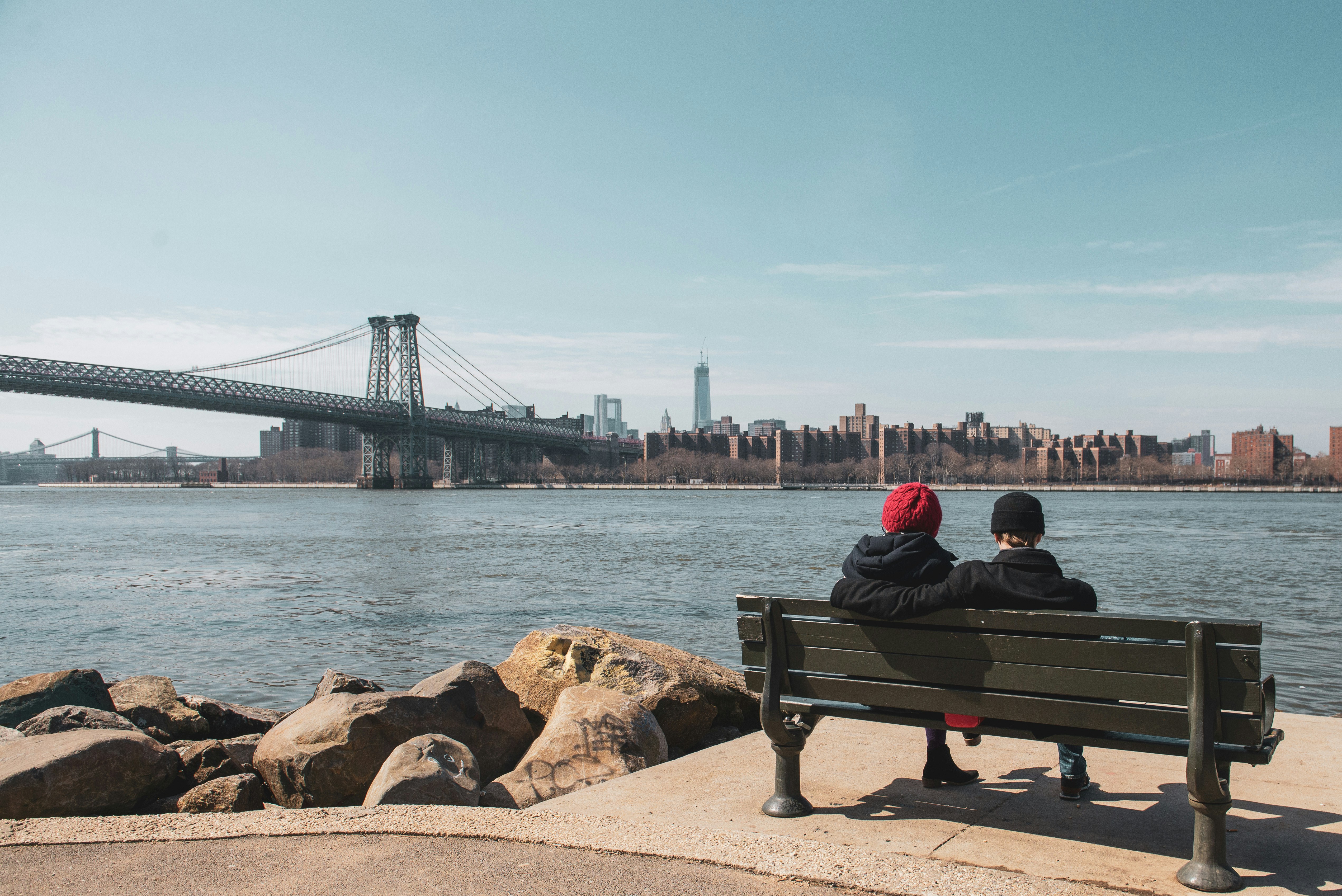 Two person sitting on outdoor bench near blue sea viewing city with ...