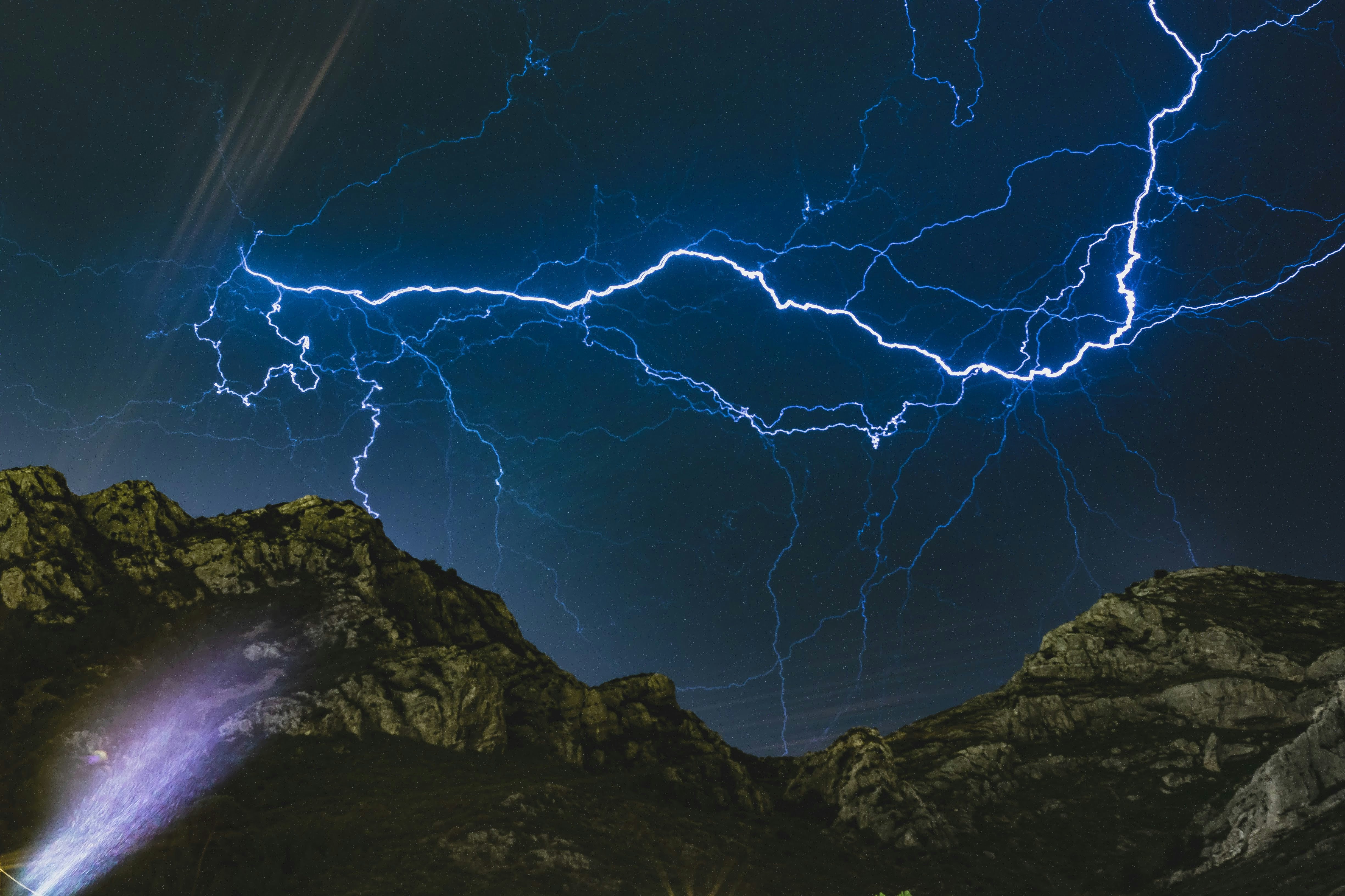 Lightning arcs dramatically across a night sky above rugged mountains.