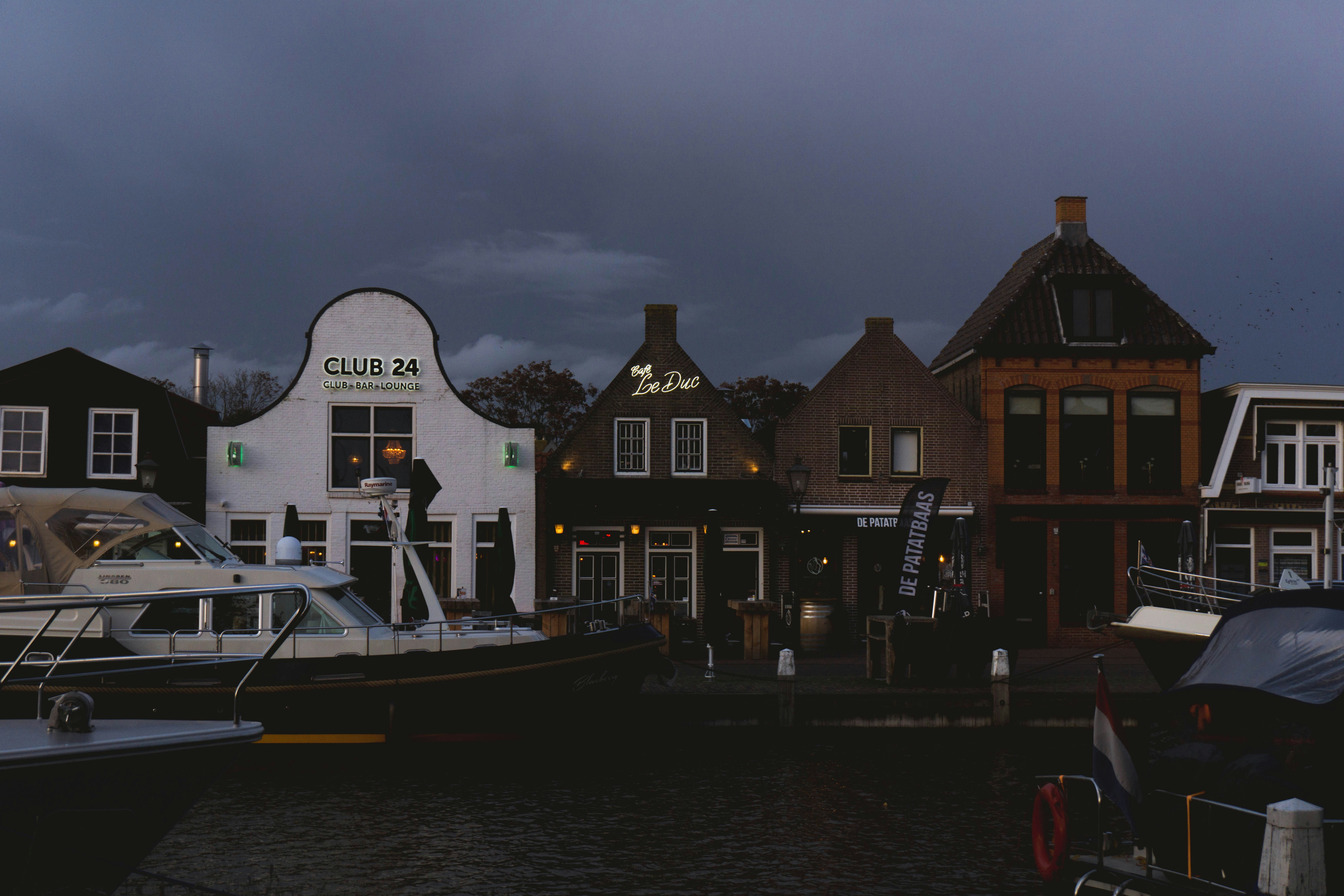 Quaint waterfront buildings reflecting the evening light, with boats anchored nearby. The scene captures a serene moment in a bustling harbor.