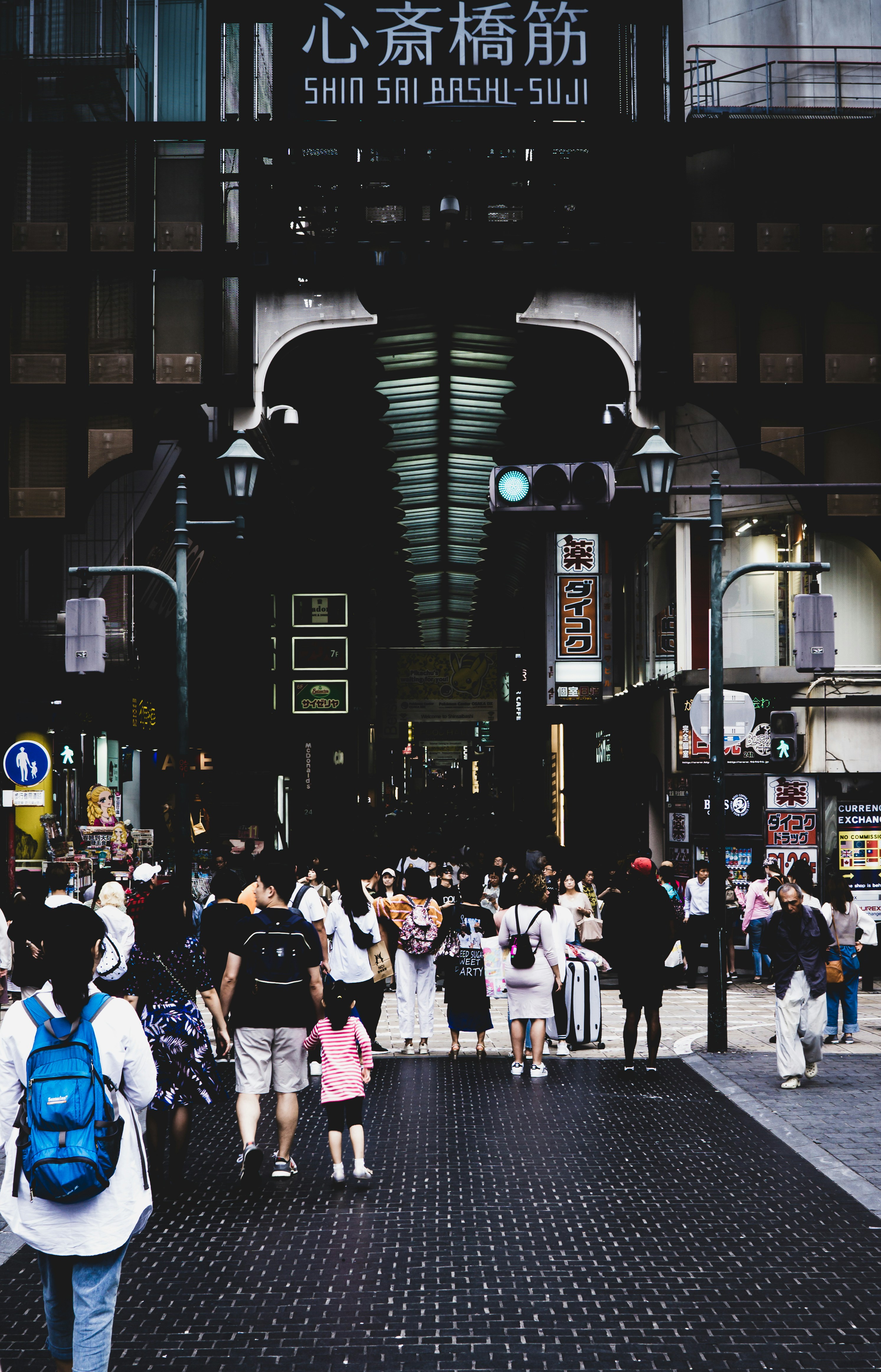 Bustling street scene in Shin Sai Bashi Suji, showcasing diverse pedestrians and vibrant storefronts under a covered arcade.
