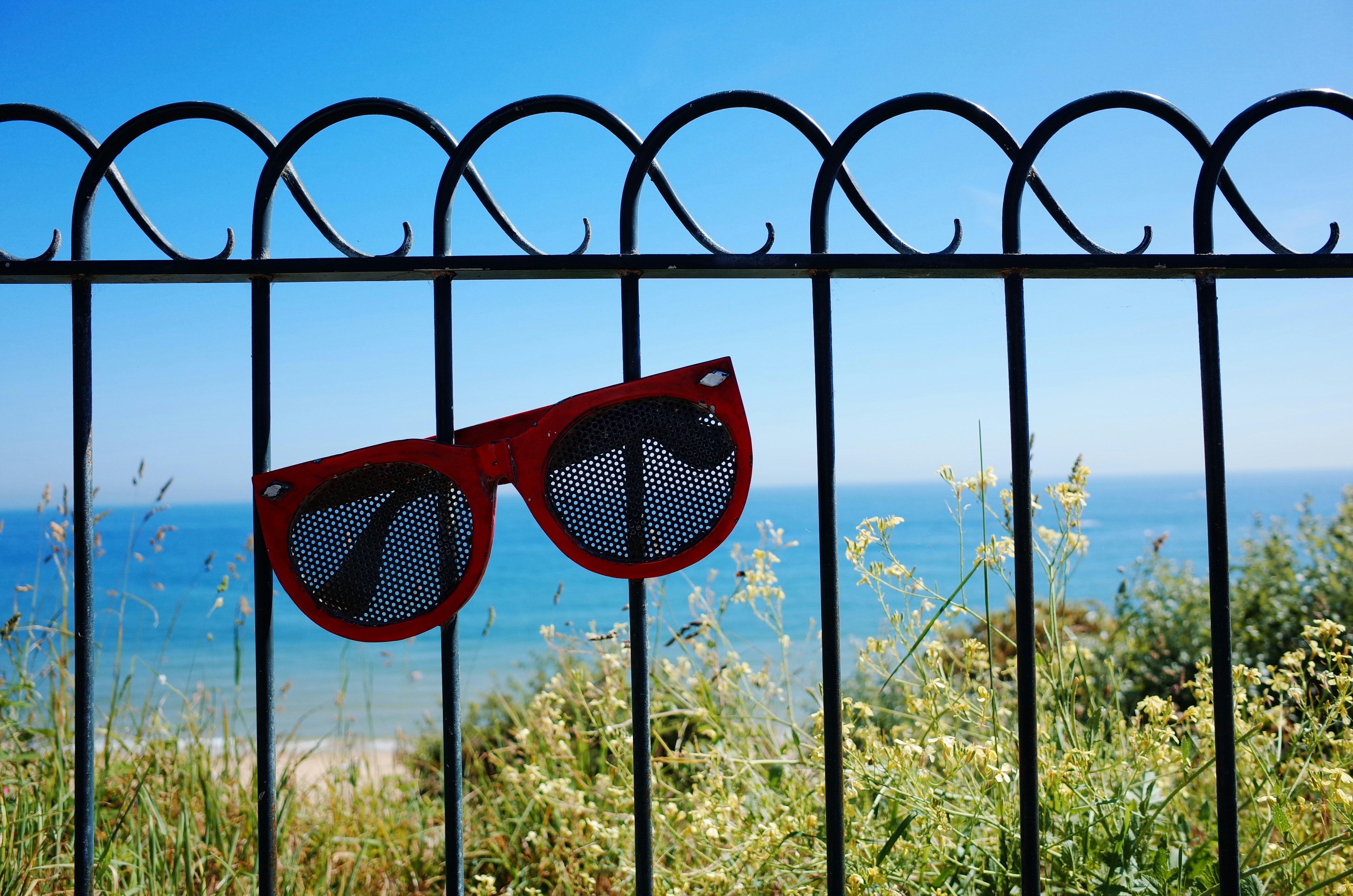 Crimson Shades on a Seaside Fence: Quiet Blue Horizon