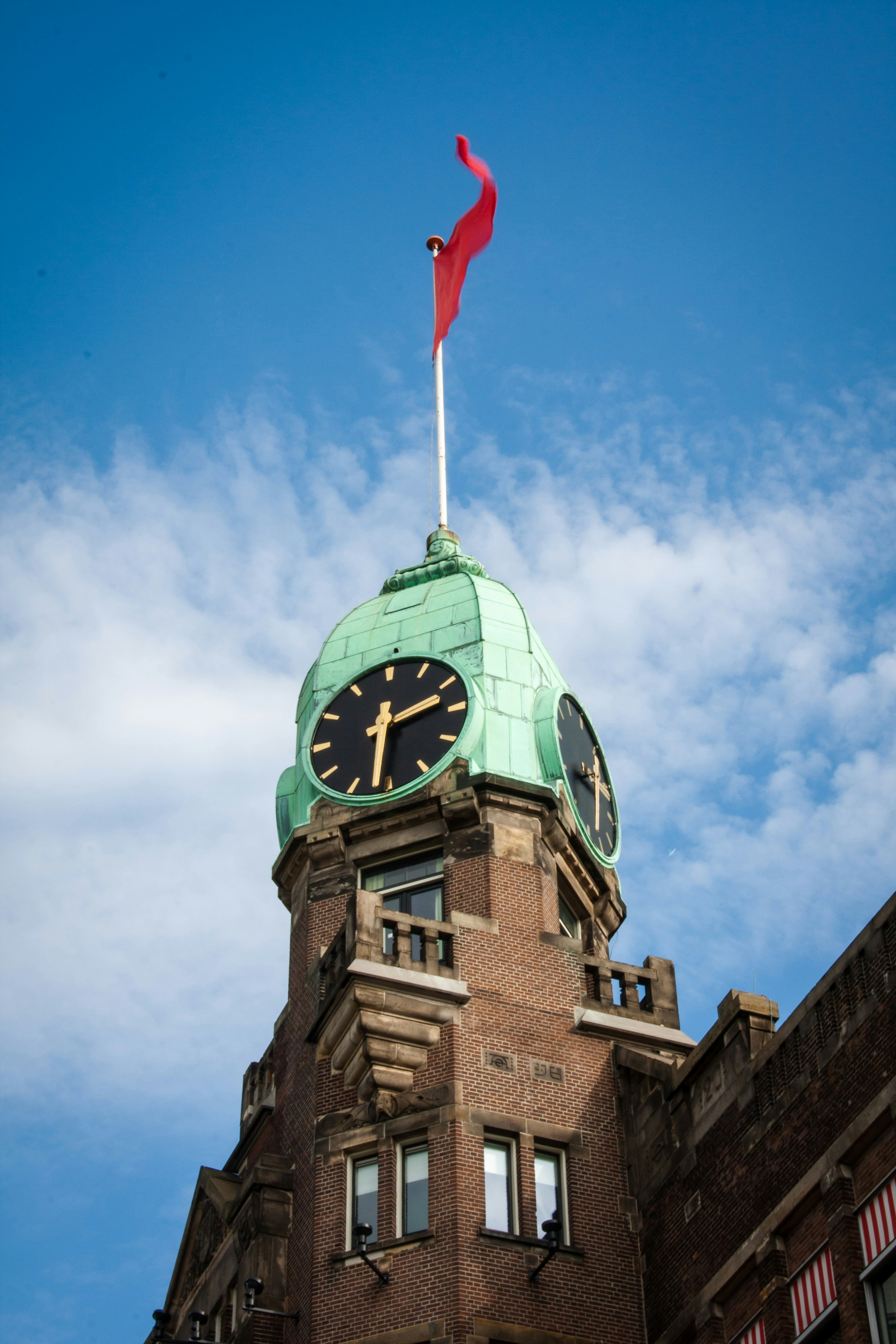 Historic clock tower adorned with a green copper dome and a red flag, set against a bright blue sky.