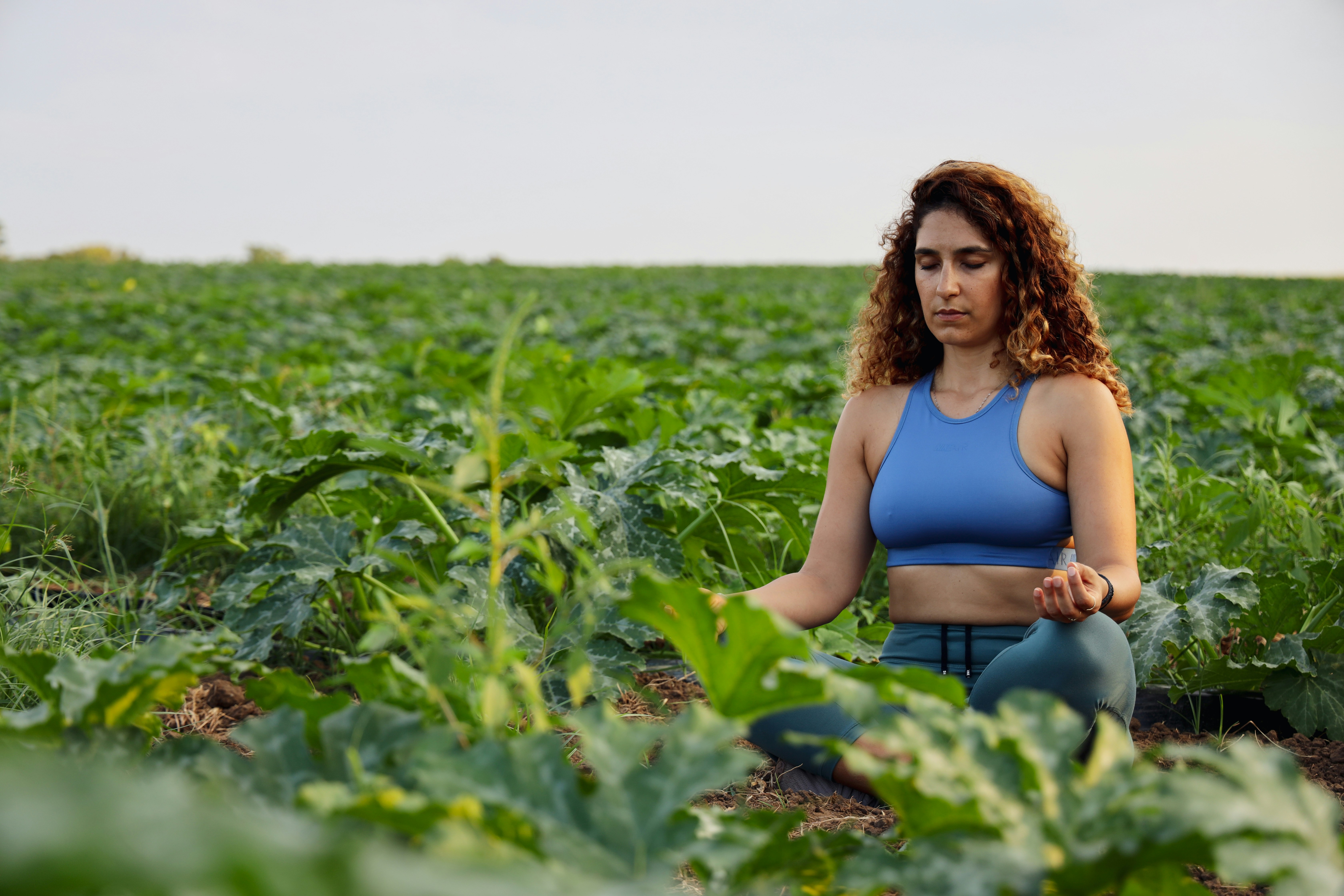 Person meditating in a lush green field under a clear sky.