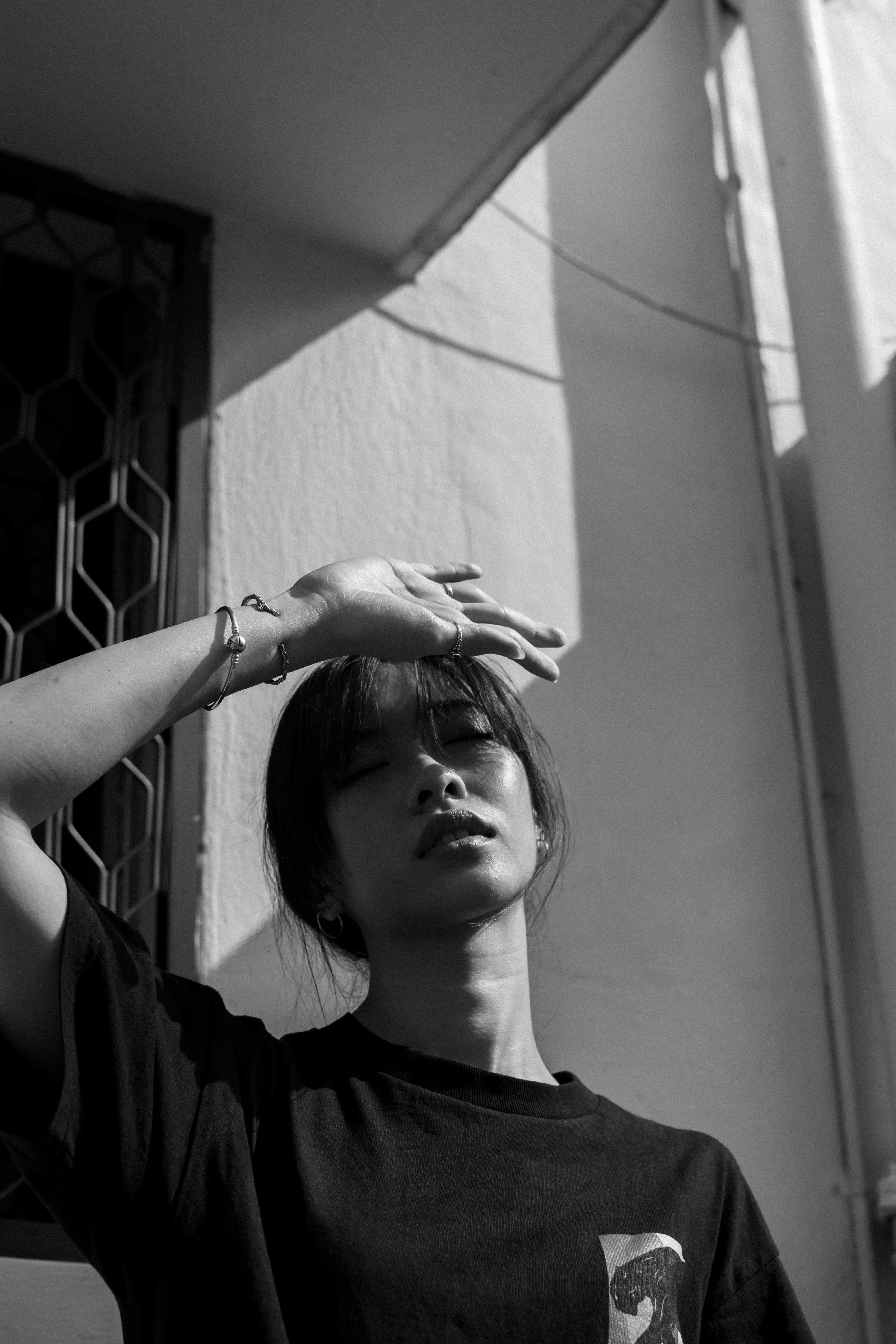 A young person shielding their eyes from the sun, framed by contrasting shadows and light. The black-and-white tones emphasize emotion and depth.