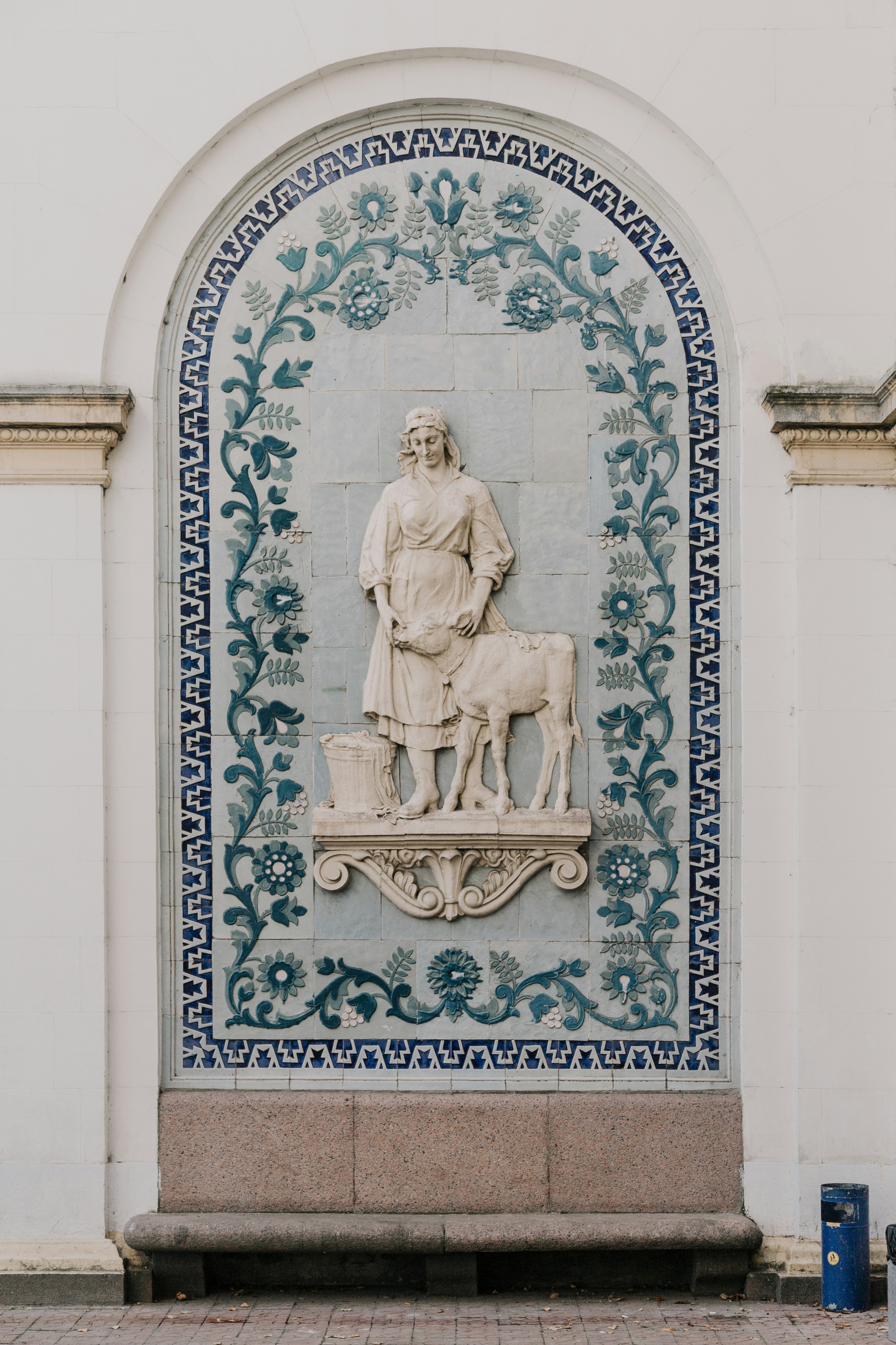 Relief sculpture depicting a farmer with a cow, surrounded by intricate floral patterns. The artwork highlights the connection between agriculture and community.