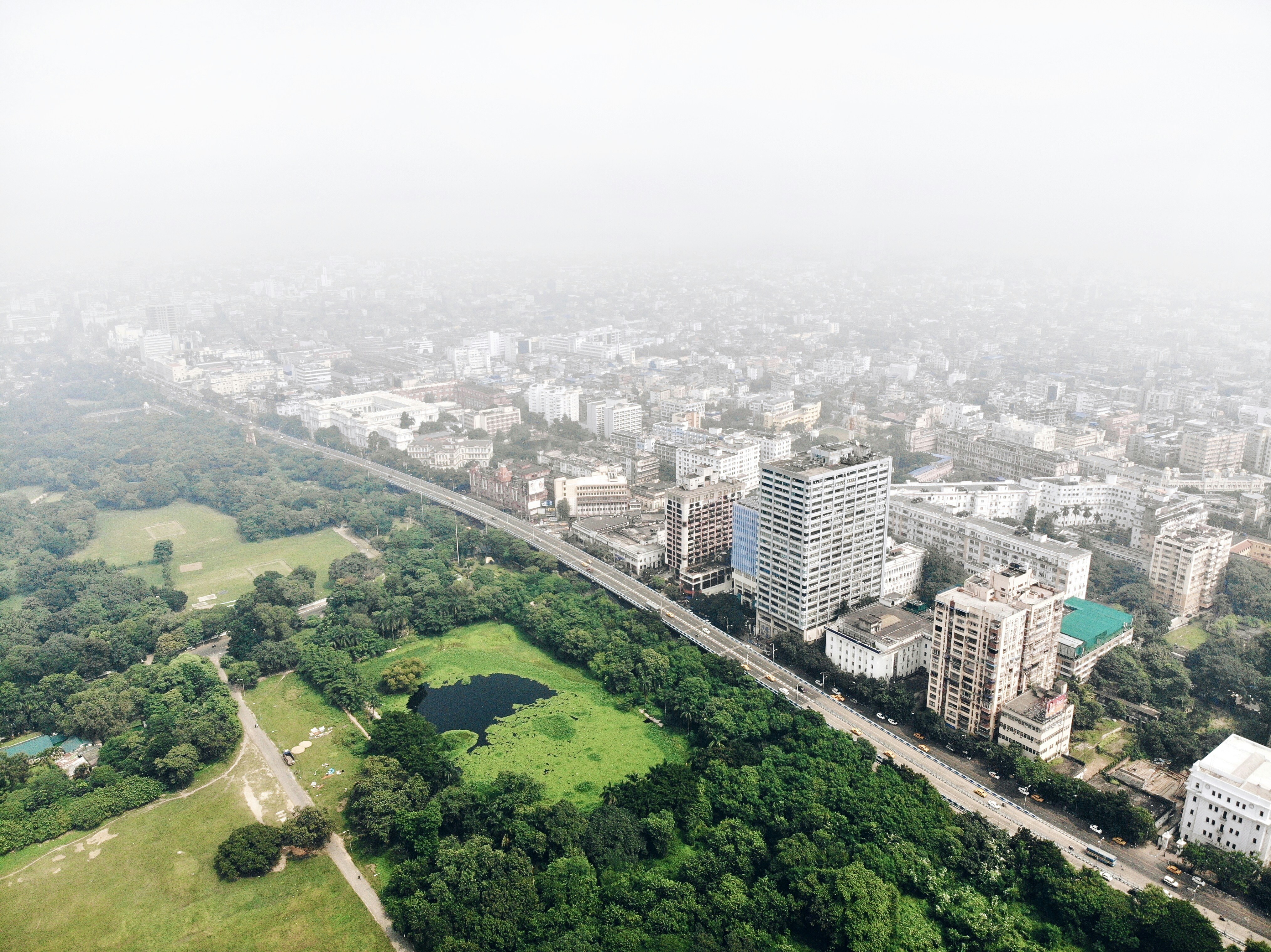 Aerial view of a cityscape with high-rise buildings adjacent to a lush, expansive park under a hazy sky.