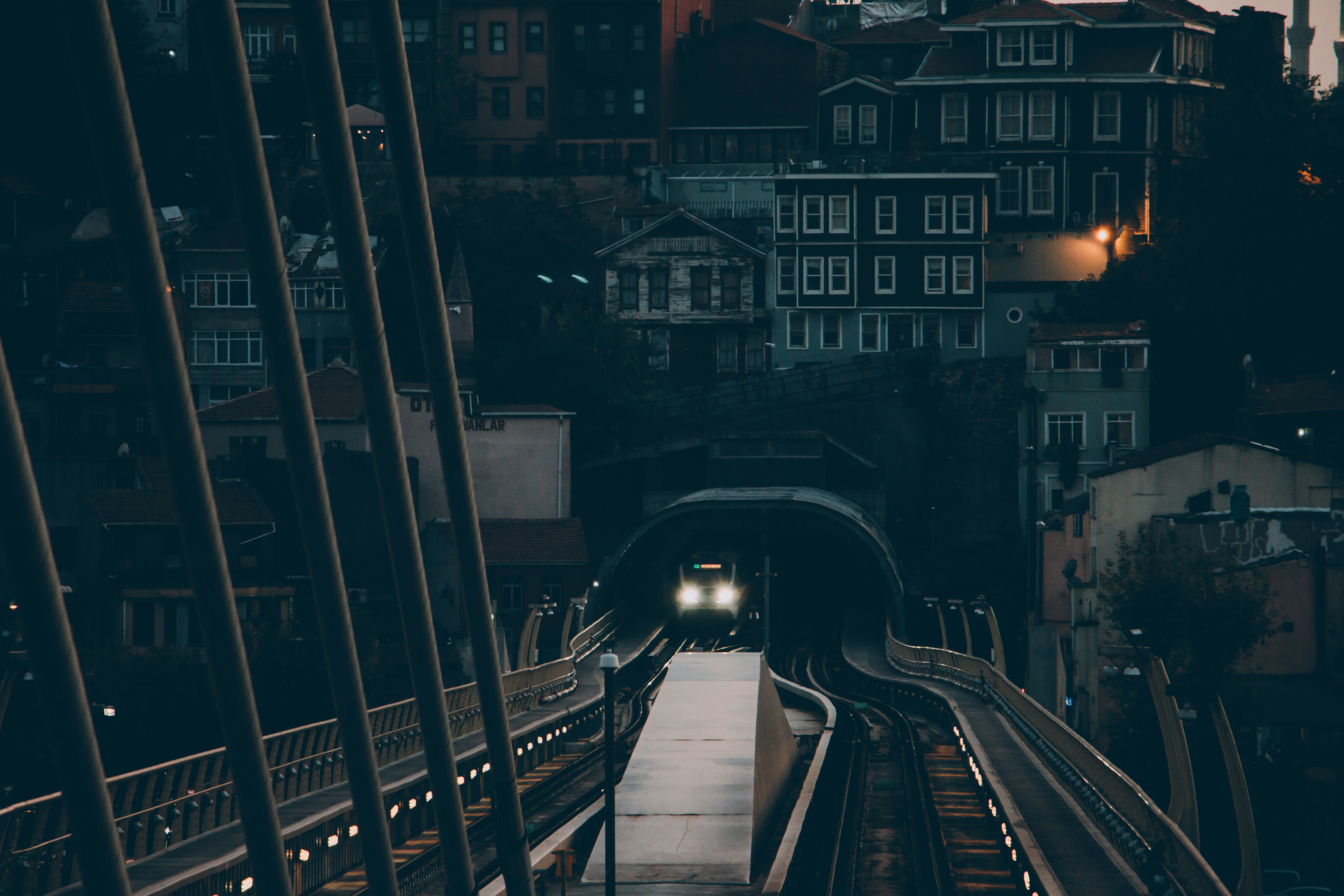 A train approaches a tunnel entrance, framed by an urban landscape at dusk, showcasing the interplay of architecture and transportation.