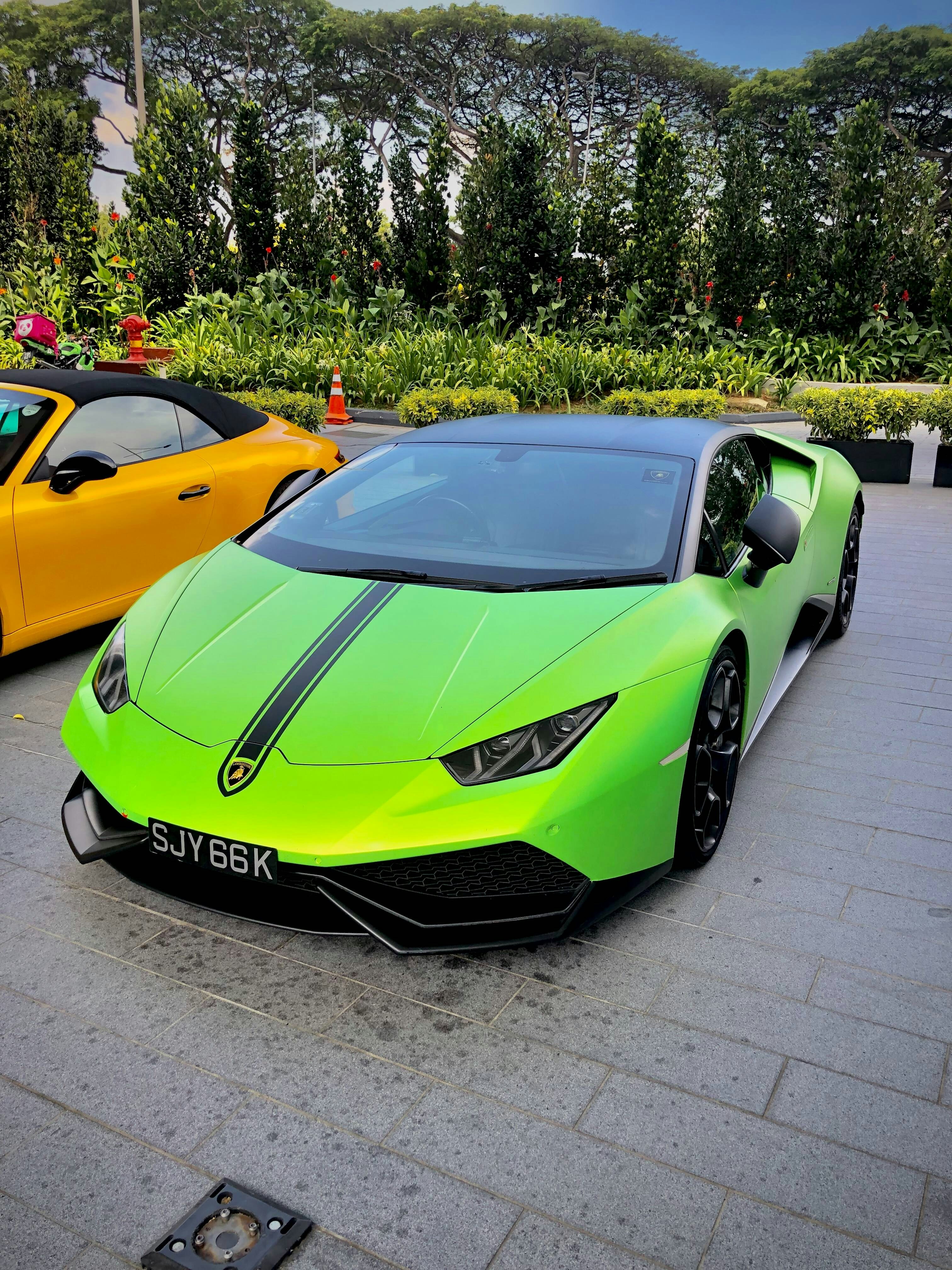 A striking green Lamborghini Huracán parked alongside a sleek yellow sports car, surrounded by lush greenery.