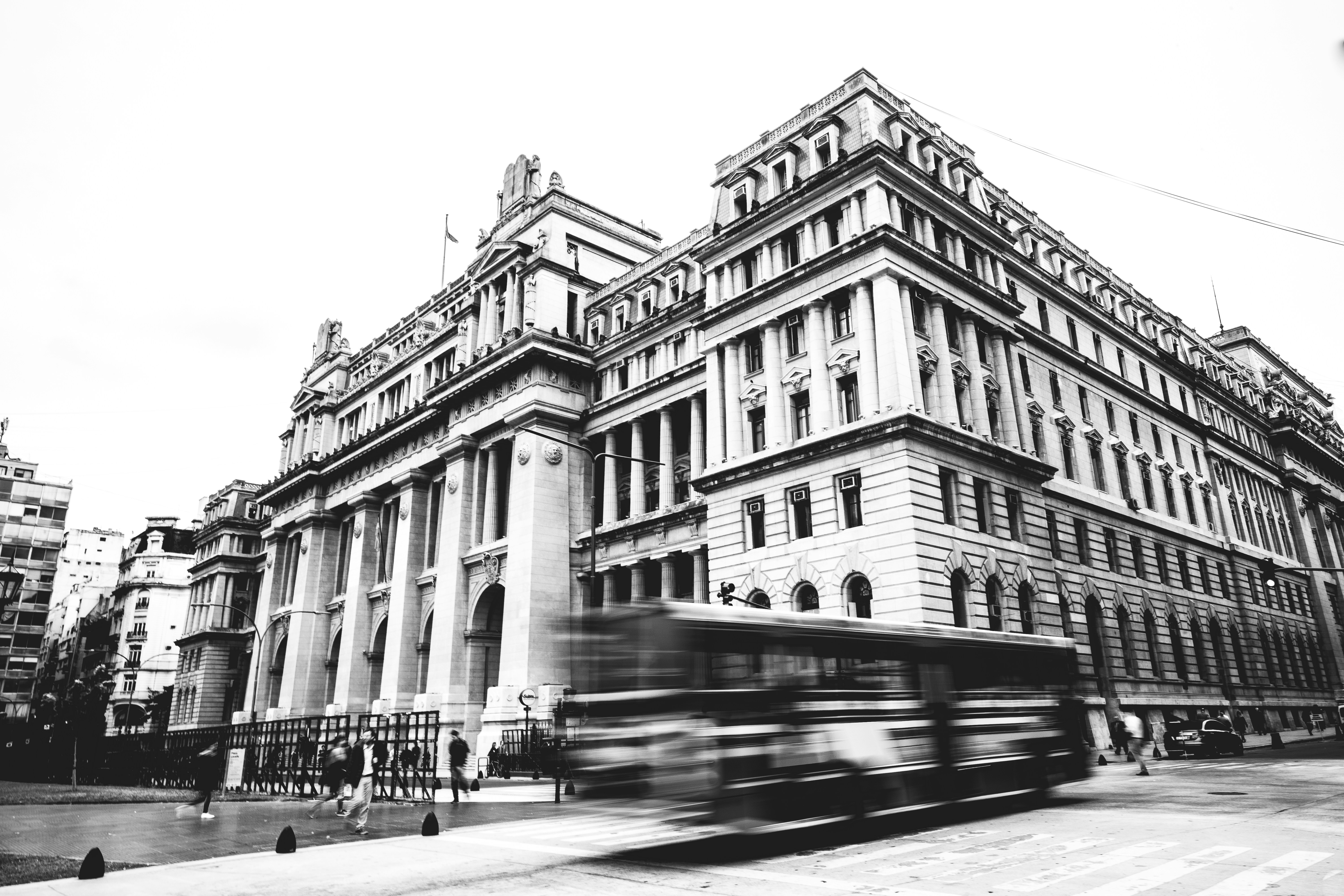Historic building juxtaposed with a moving tram in a black-and-white cityscape, highlighting urban life and architectural grandeur.