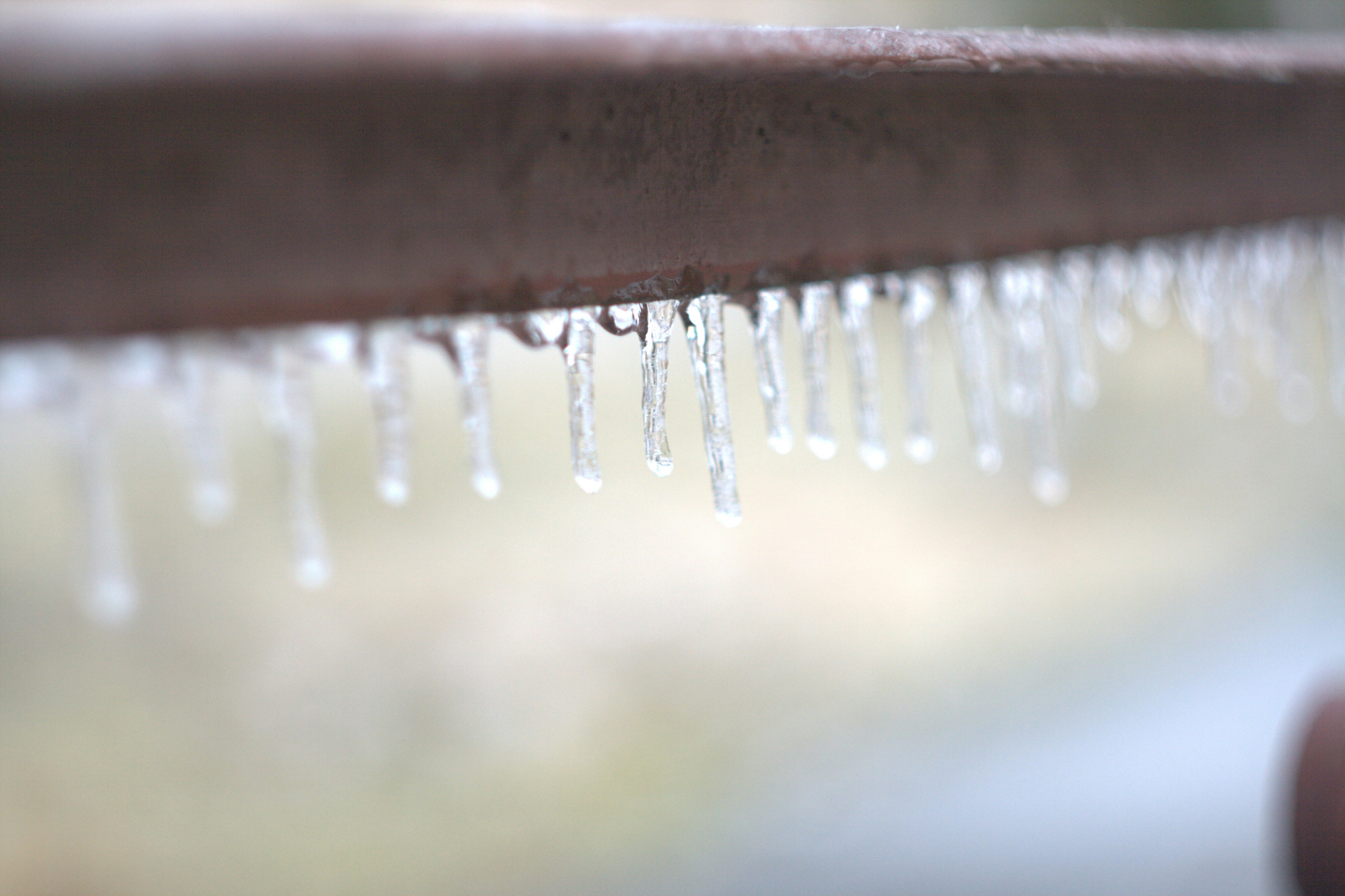 Icicles hanging from a metal railing, glistening in soft light against a blurred natural background.