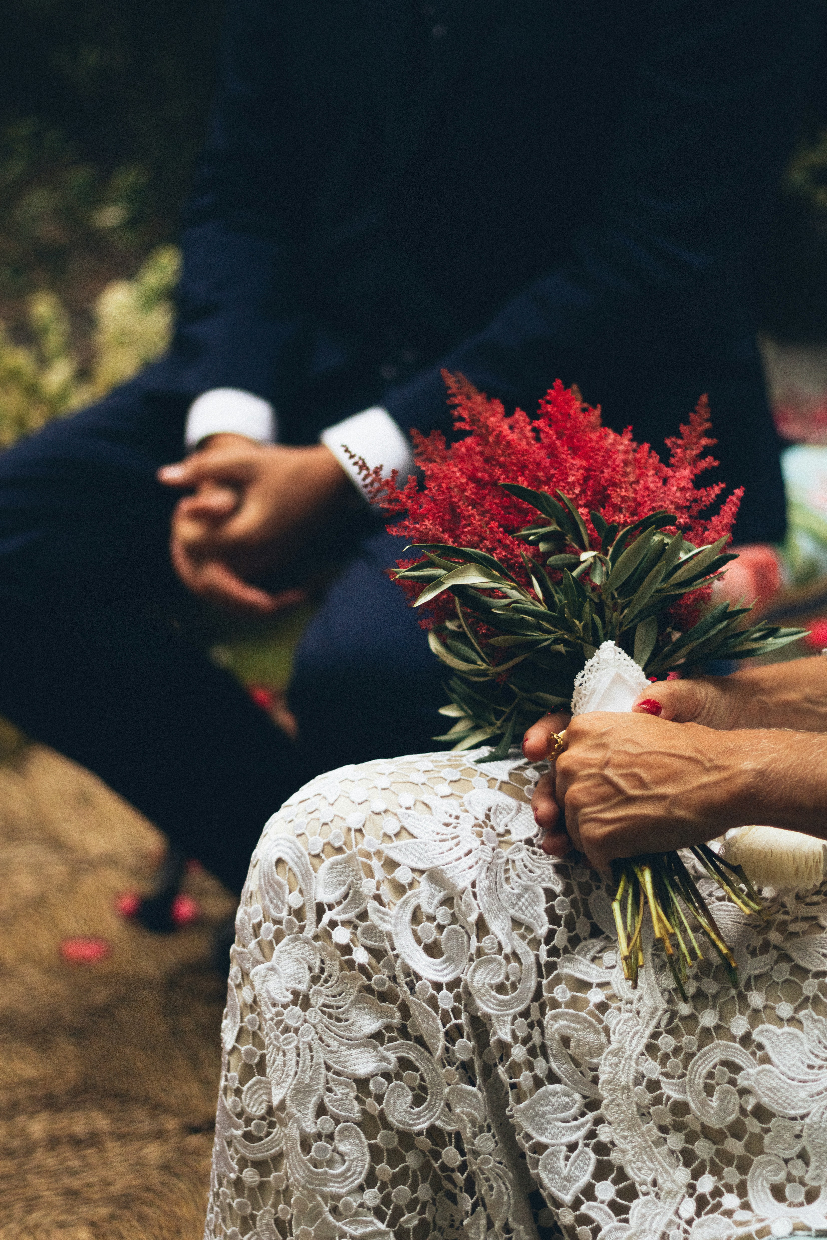 A close-up of a hand holding a vibrant bouquet of red flowers, contrasted against a delicate lace dress, symbolizing love and celebration.