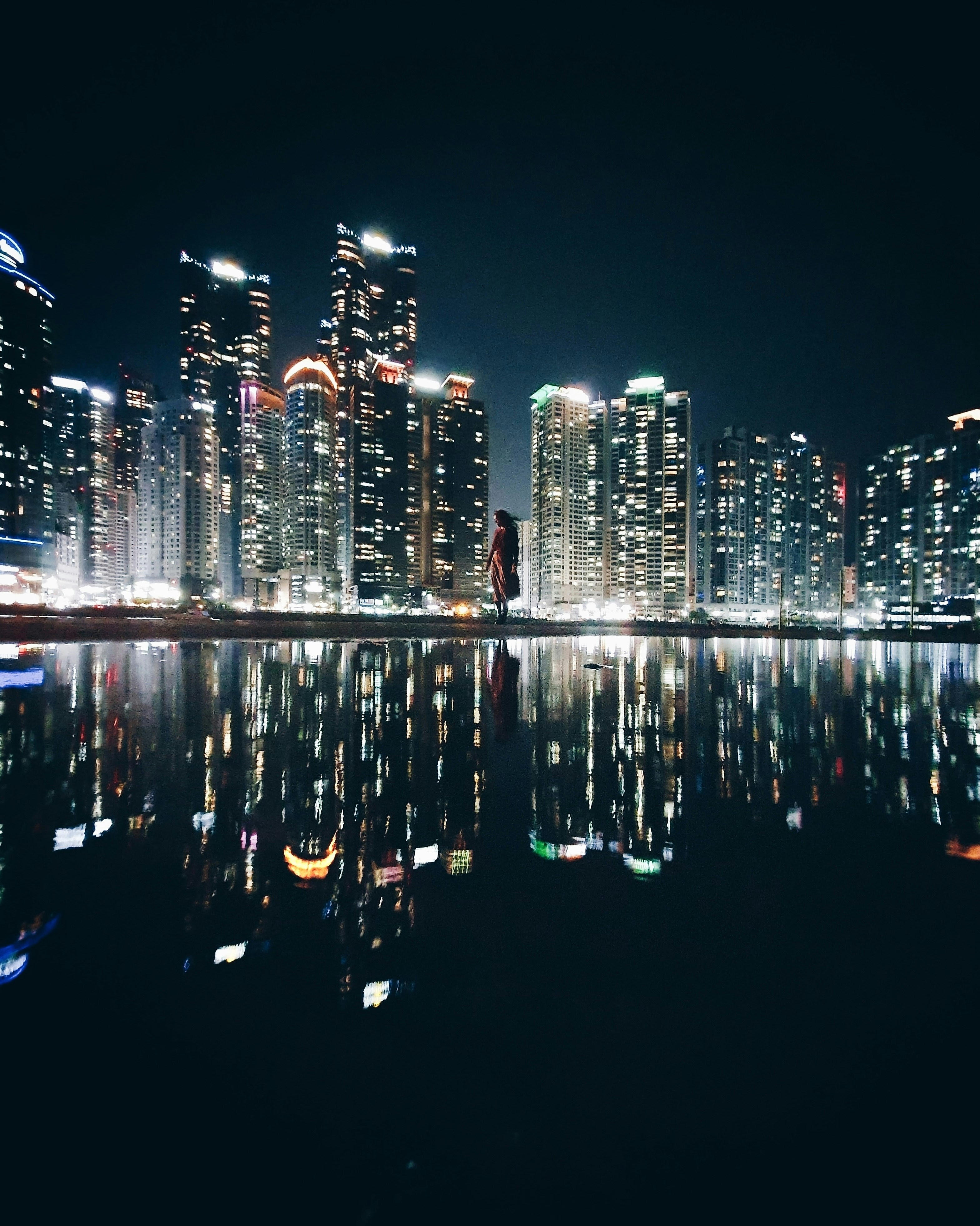 Reflection of high-rise buildings on body of water during nighttime ...