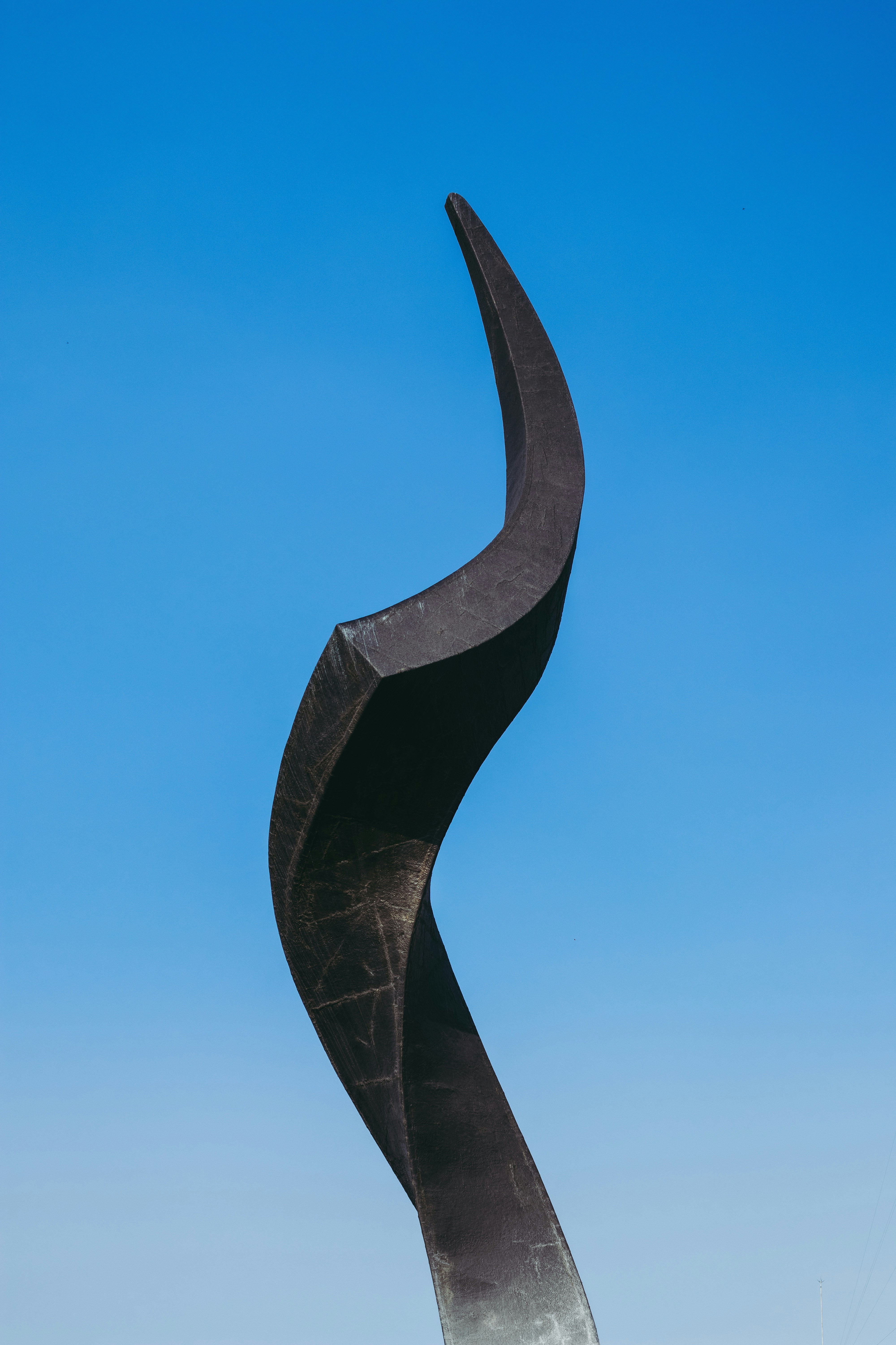 A sleek, abstract sculpture reaching towards the sky, contrasting sharply against a clear blue backdrop.