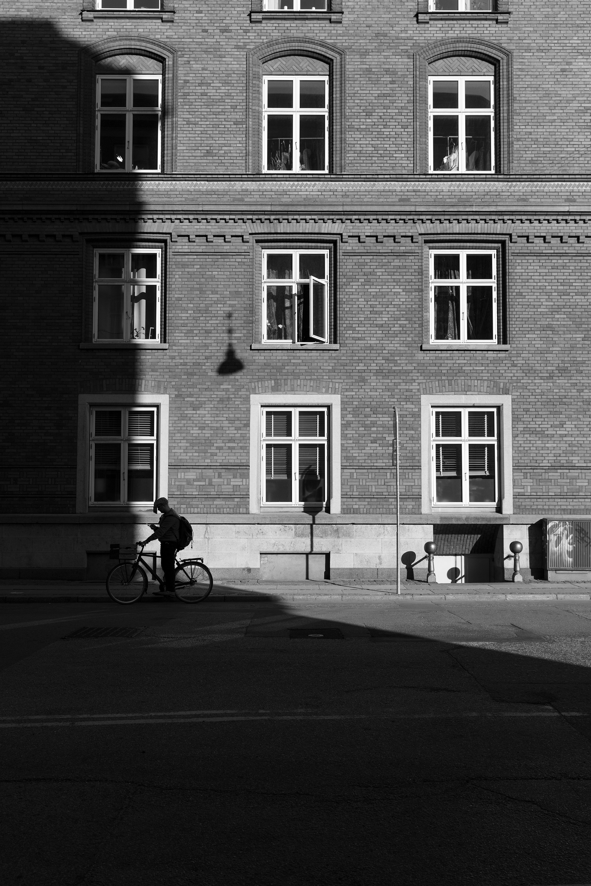 A cyclist navigates the street alongside a brick building, casting long shadows in the early evening light.
