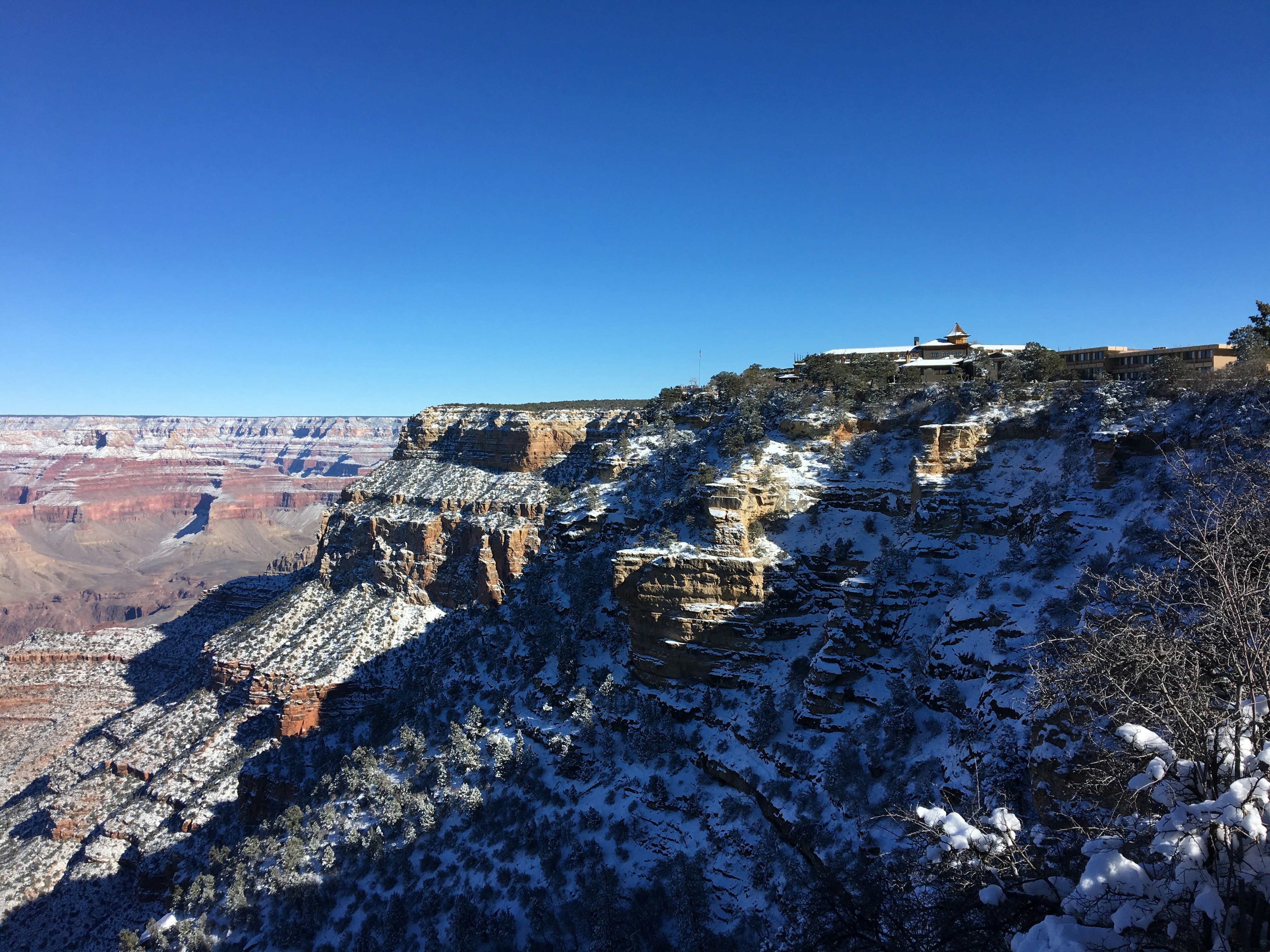 Snow-covered cliffs of the Grand Canyon under a clear blue sky, highlighting the contrast between the icy landscape and the warm hues of the canyon's rock formations.