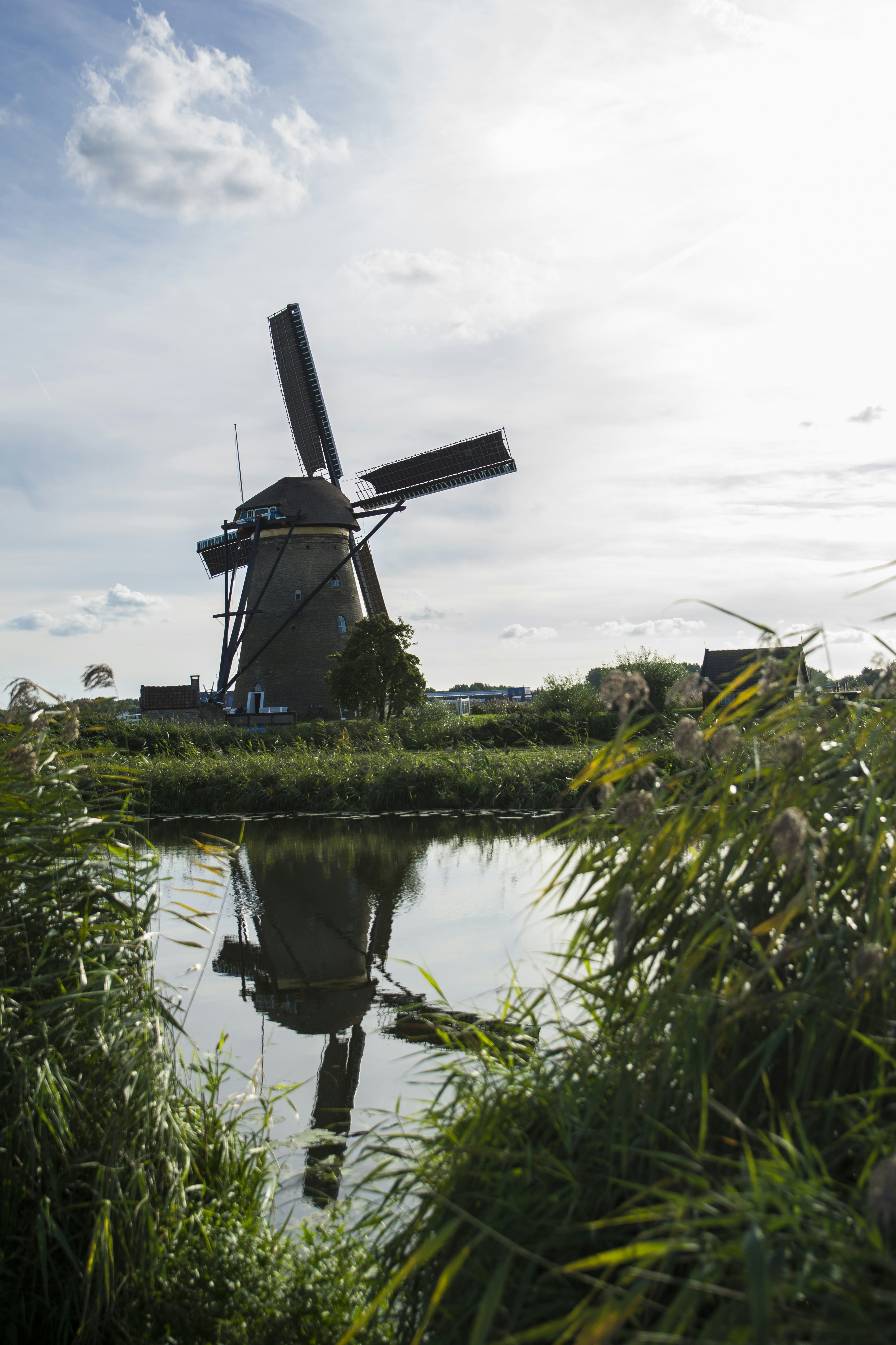 Historic windmill reflected in a serene canal under a cloudy sky.