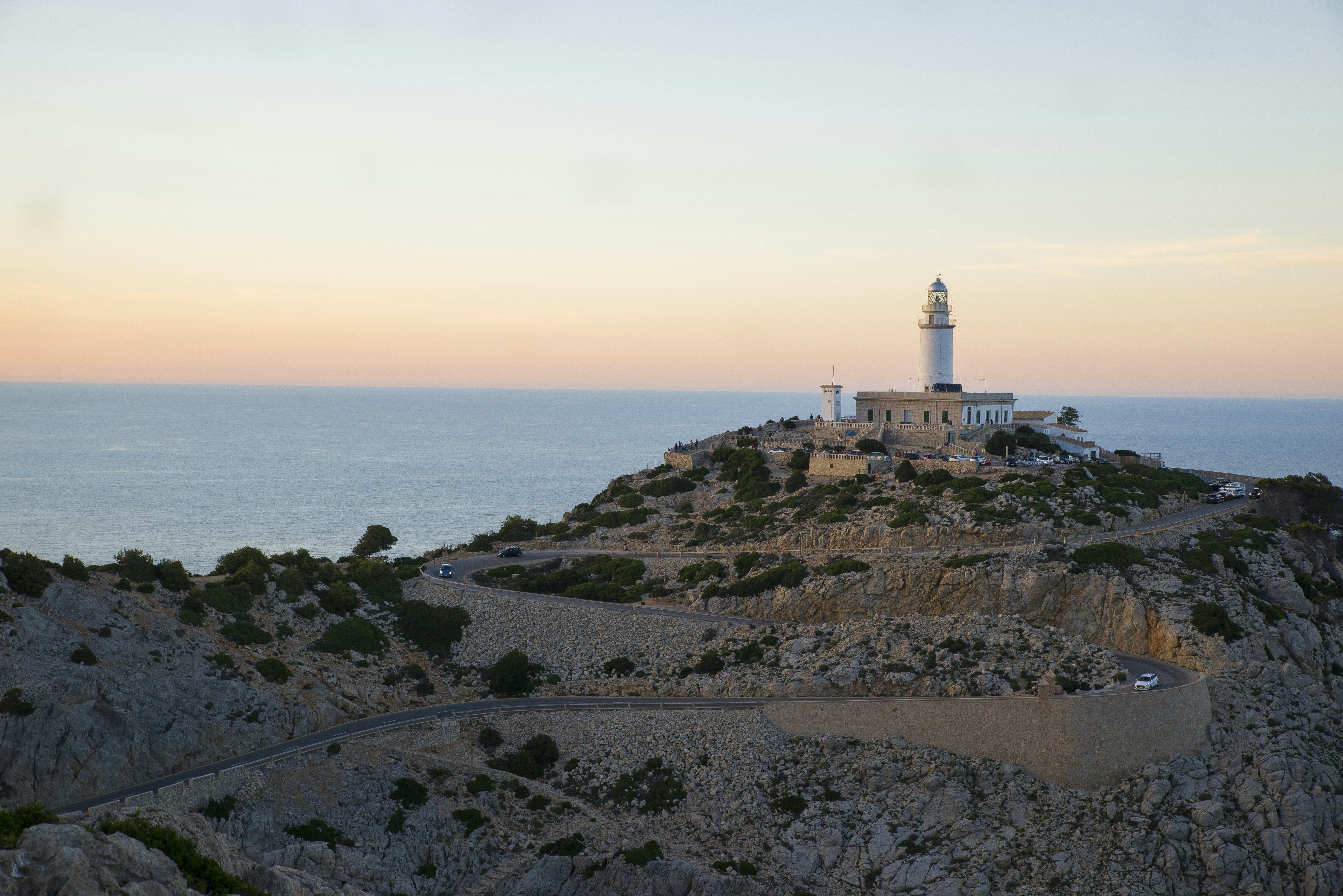 Lighthouse perched on a rugged cliff overlooking the sea under a pastel sky at sunset.