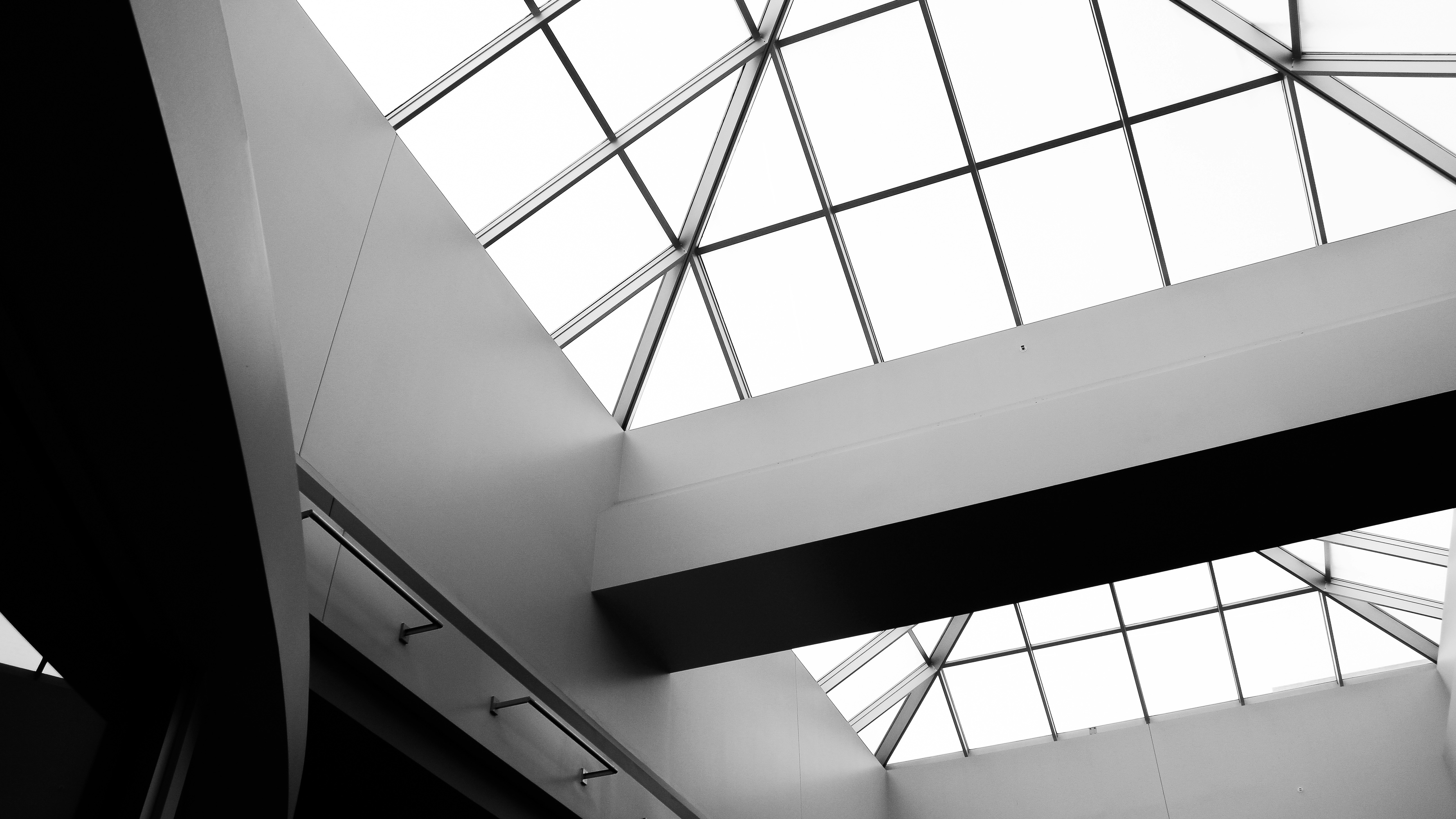 Monochrome view of a geometric skylight with intersecting beams and glass panels.