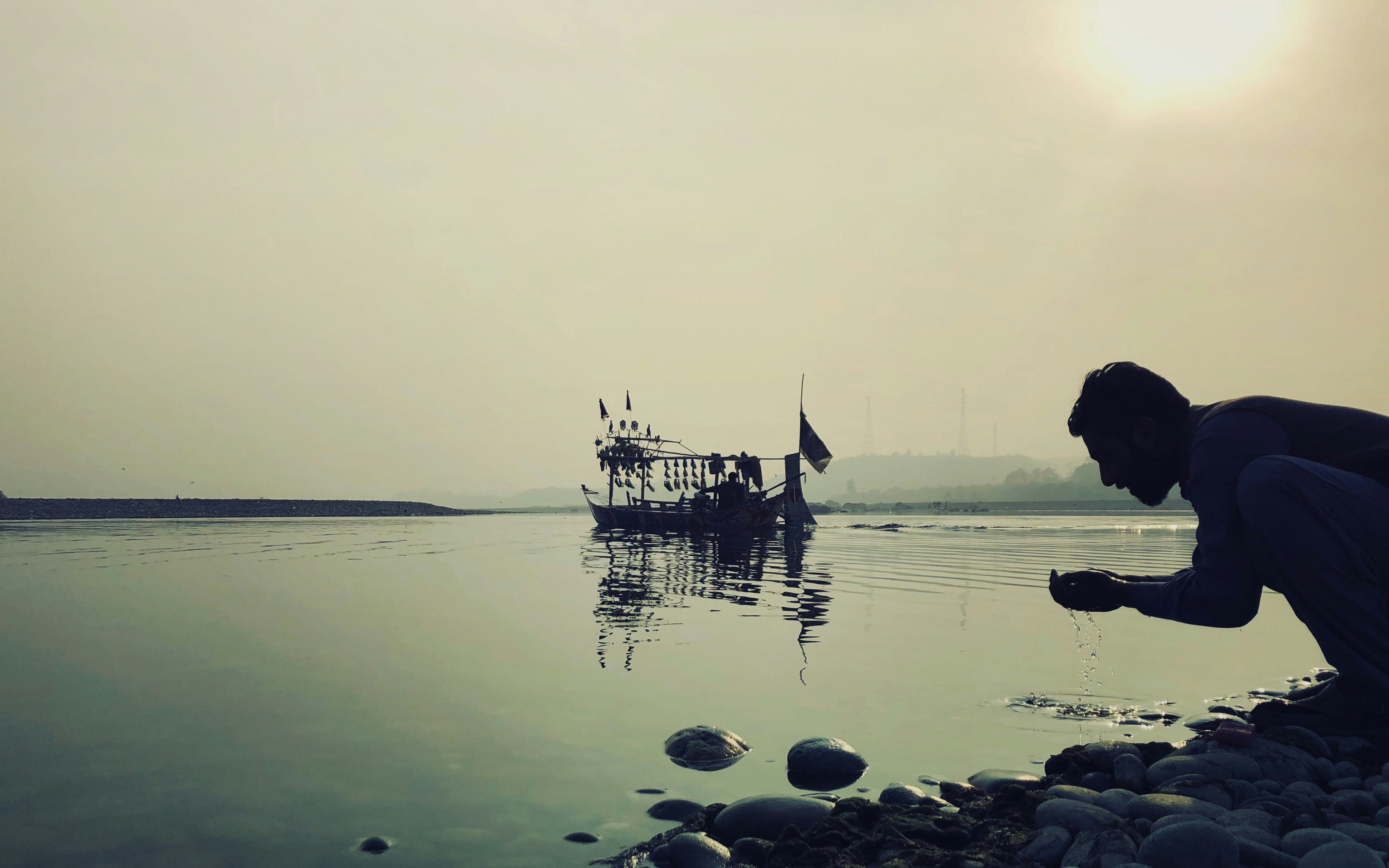 Silhouette by the Shore: a Quiet Moment with a Distant Boat