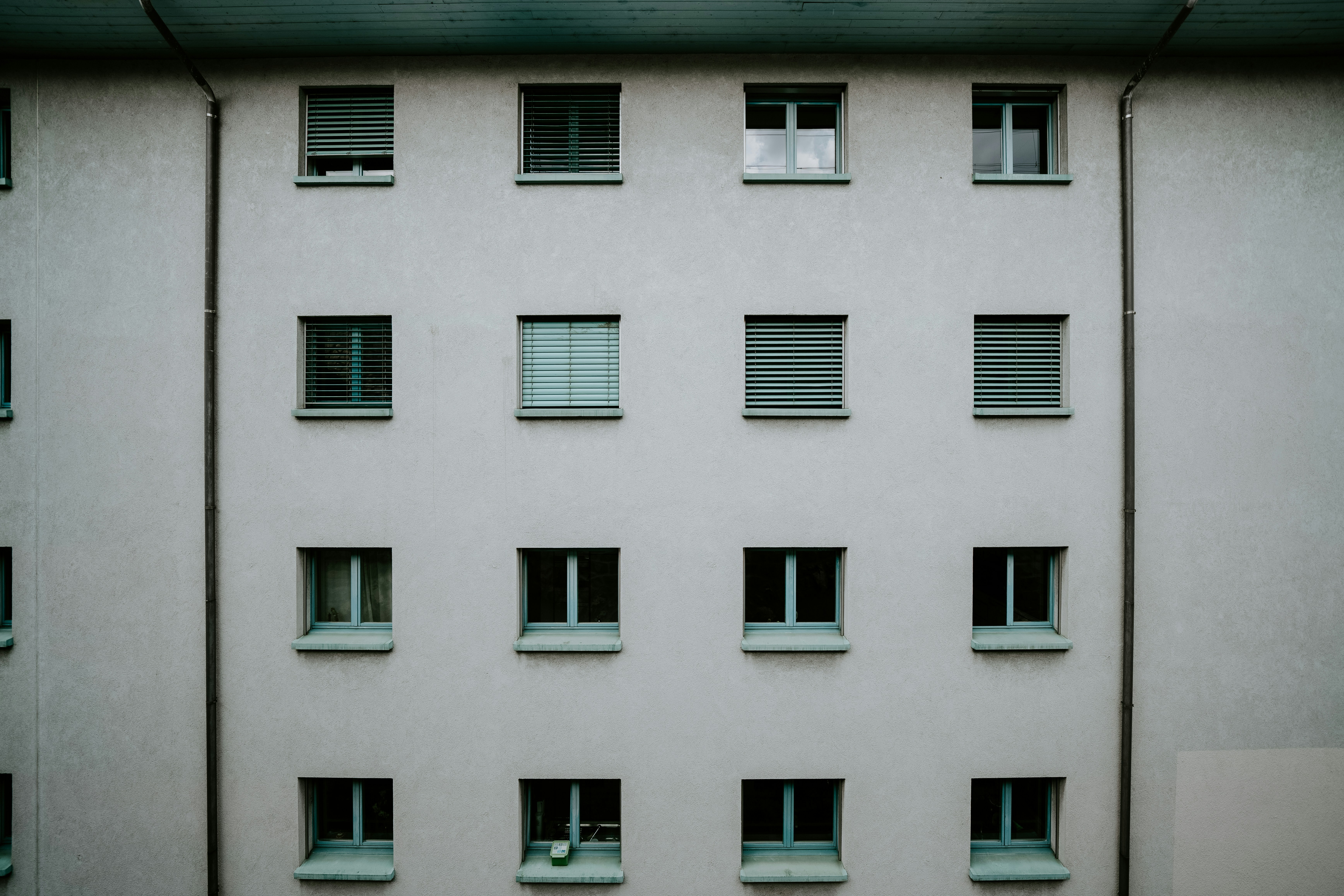 A minimalist view of a residential building's facade, showcasing a pattern of windows and shutters against a muted backdrop.