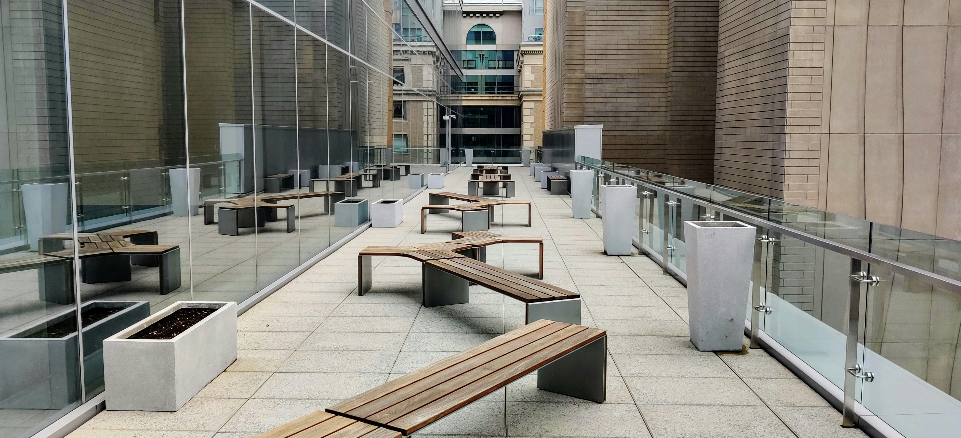 Long, modern terrace with wooden benches and glass walls, receding toward a central doorway; scene emphasizes architectural rhythm and symmetry.