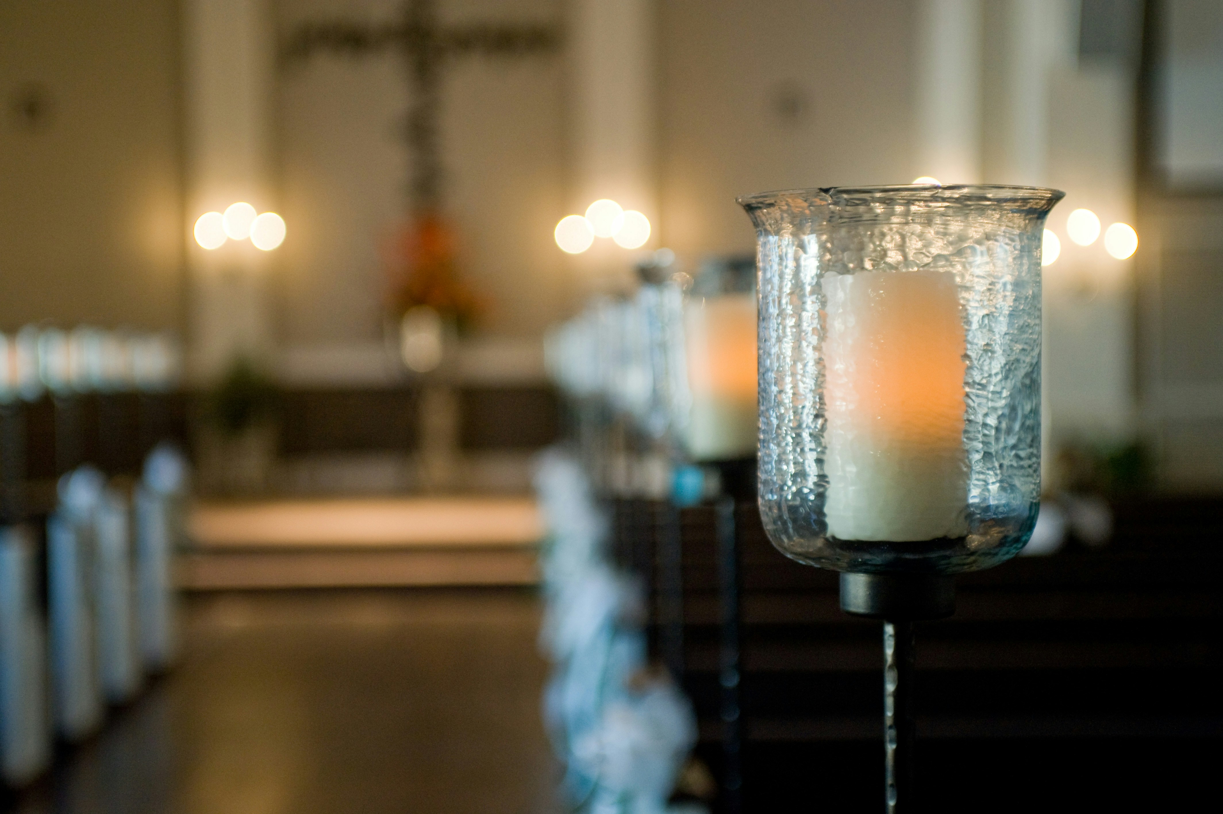 Elegant candle holders line a tranquil aisle, casting a warm glow in a serene indoor setting. The soft focus enhances the peaceful atmosphere.