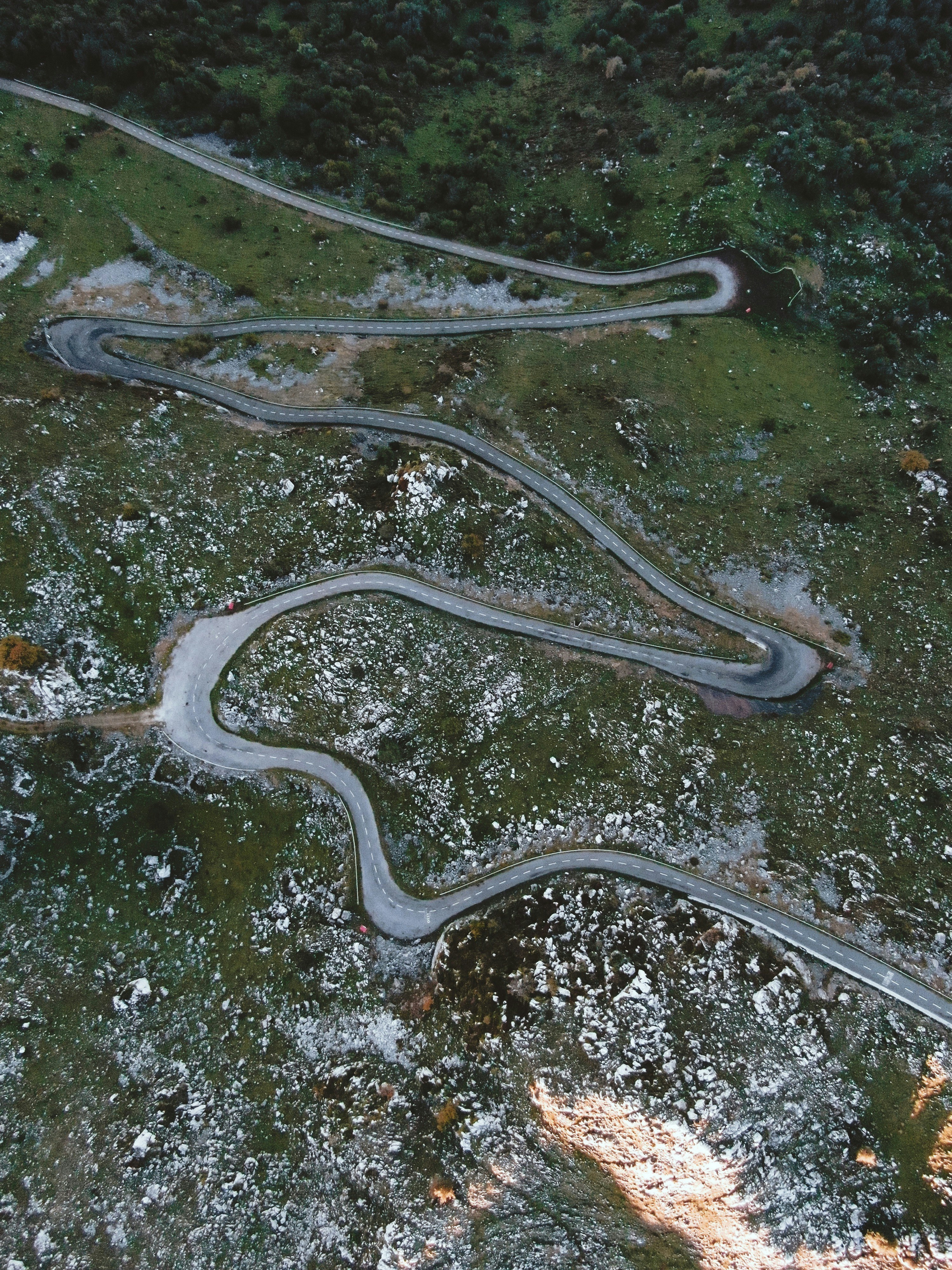 Aerial view of a winding road meandering through lush green terrain, showcasing the contrast between the asphalt and the surrounding nature.